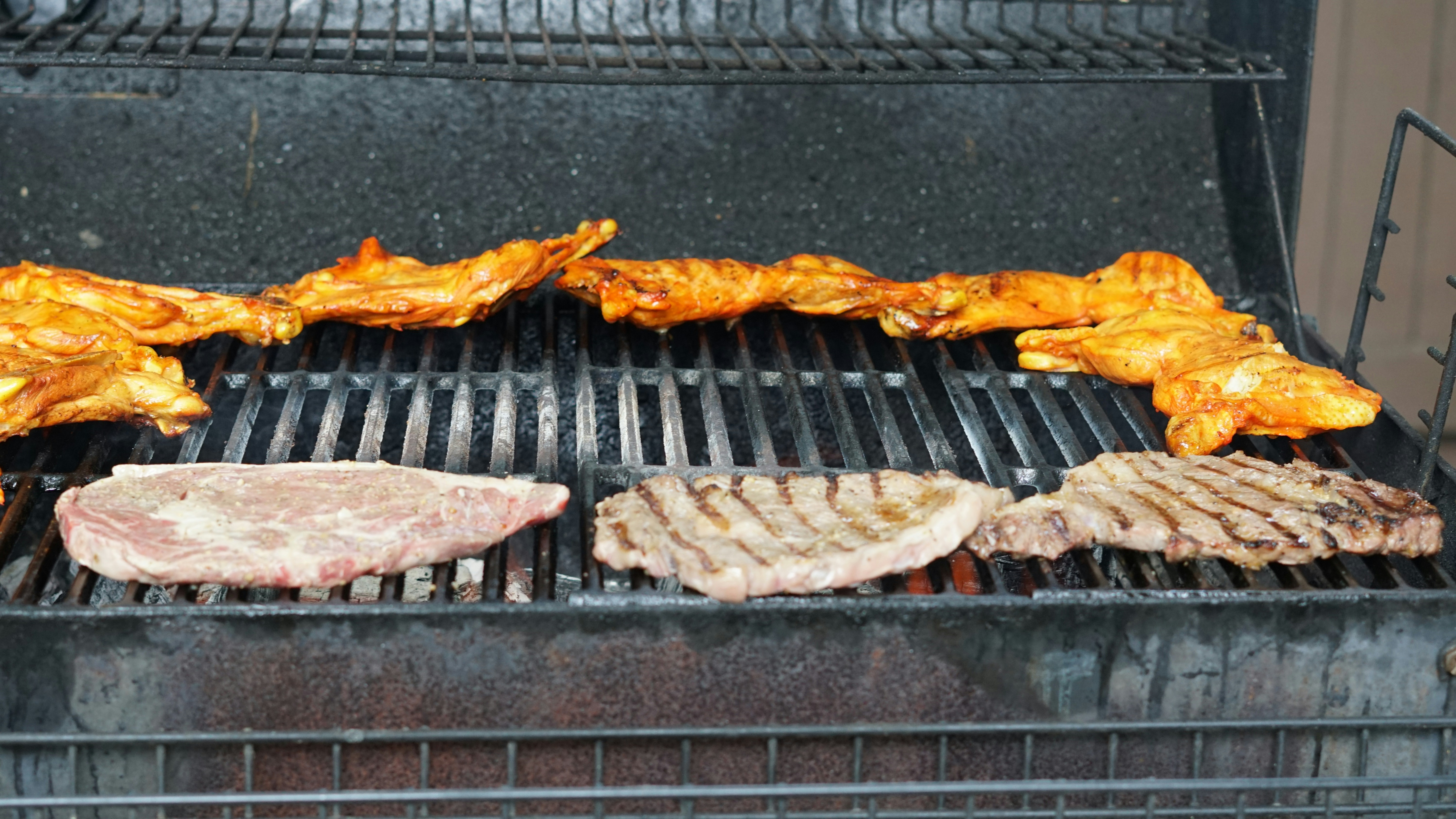Sizzling meat strips cook on an open grill with orange smoke rising along the grate.