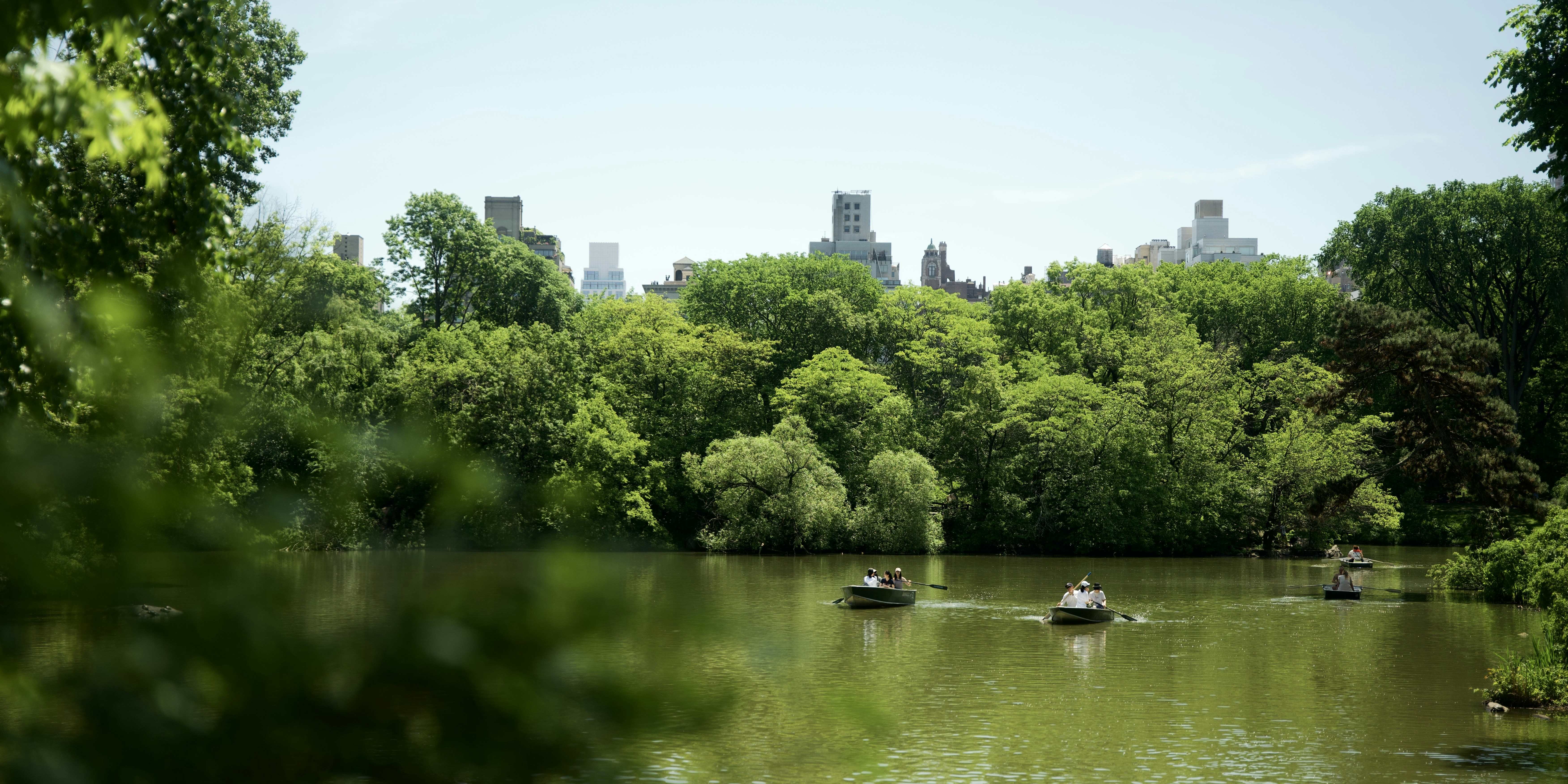 Boaters on a park lake with a distant city skyline.