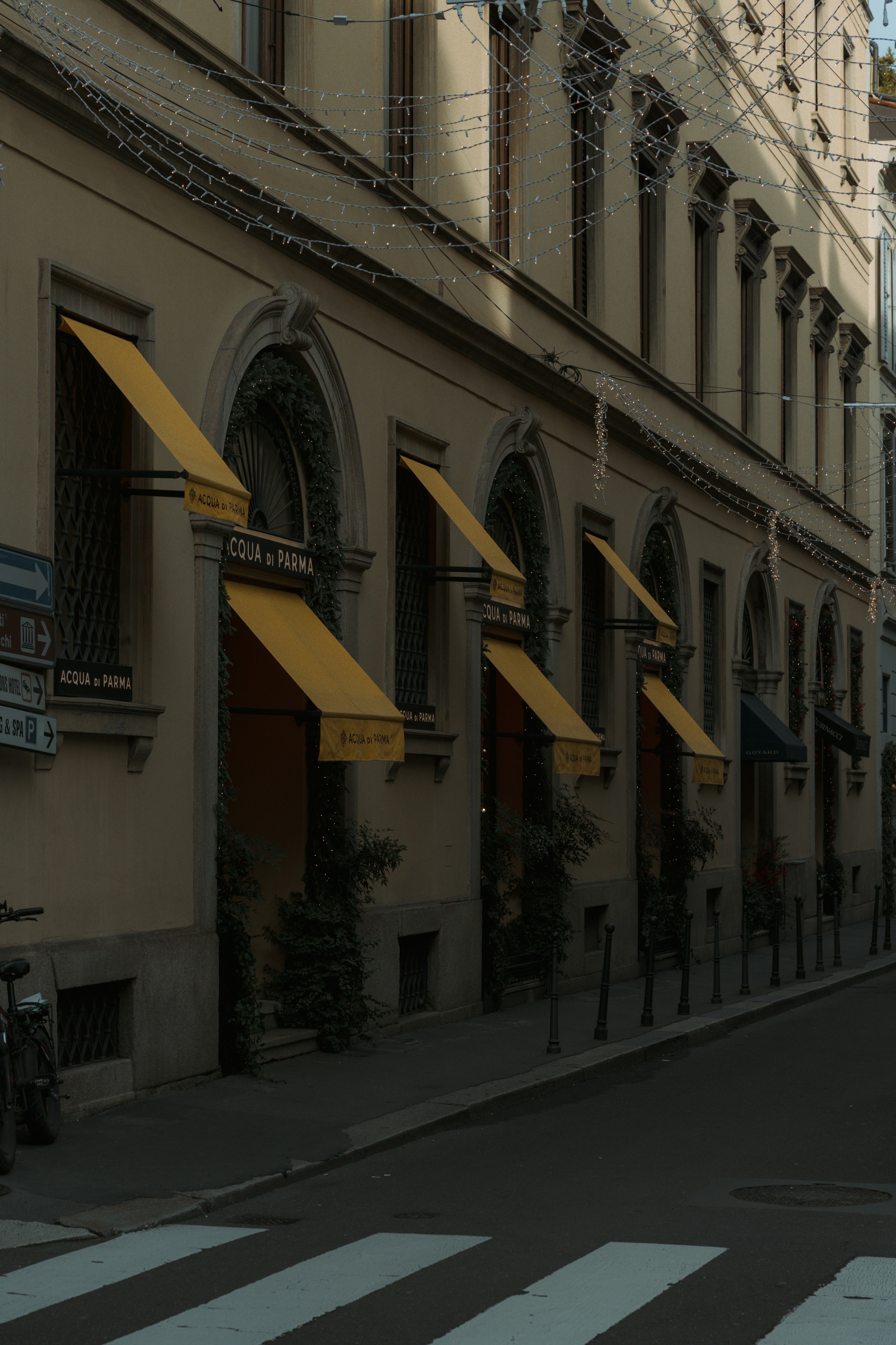 Quiet city street with buildings, yellow awnings, and string lights.