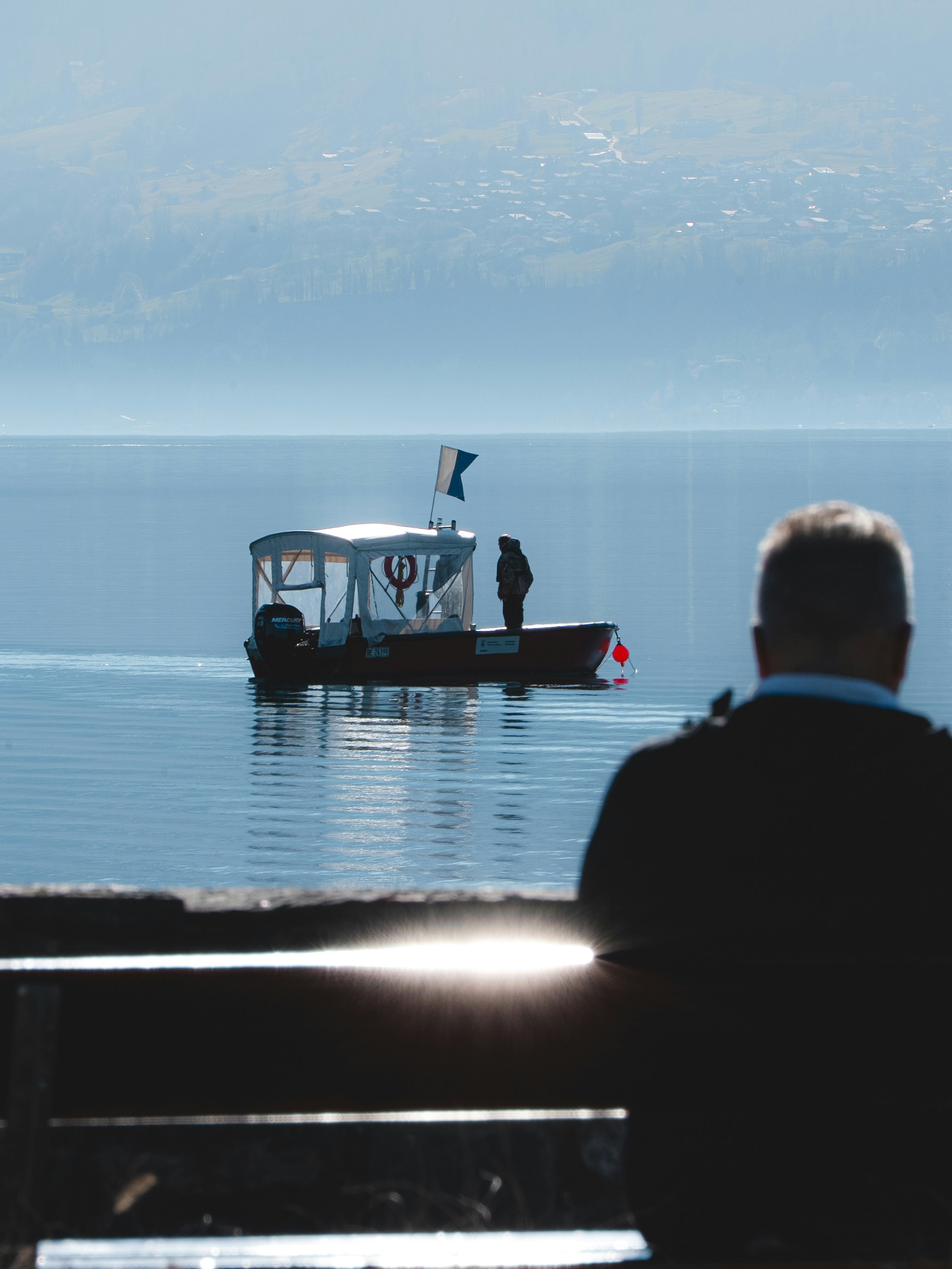 Boat on still lake with distant hills and a contemplative figure in foreground