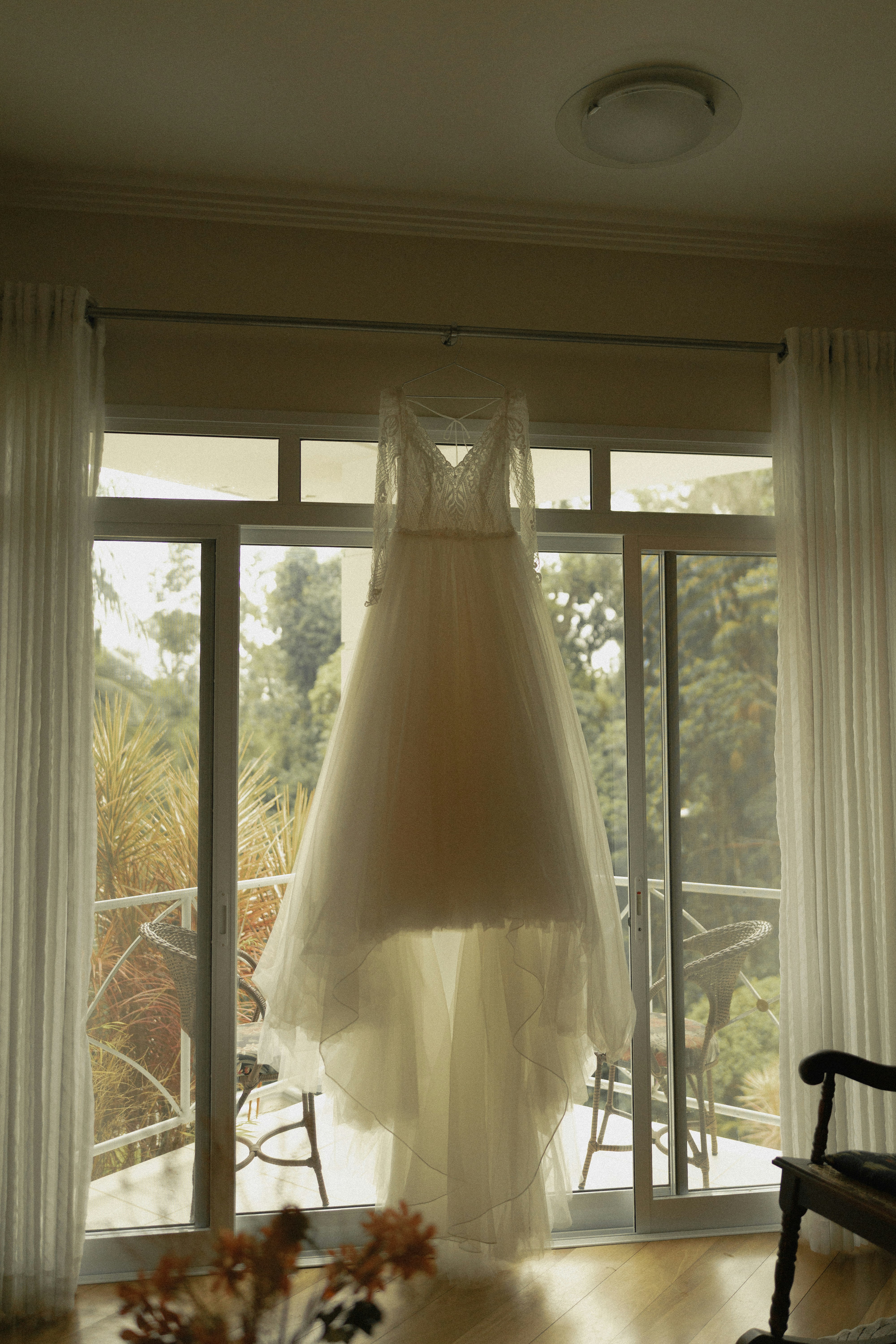 A white wedding dress hangs by a large window.