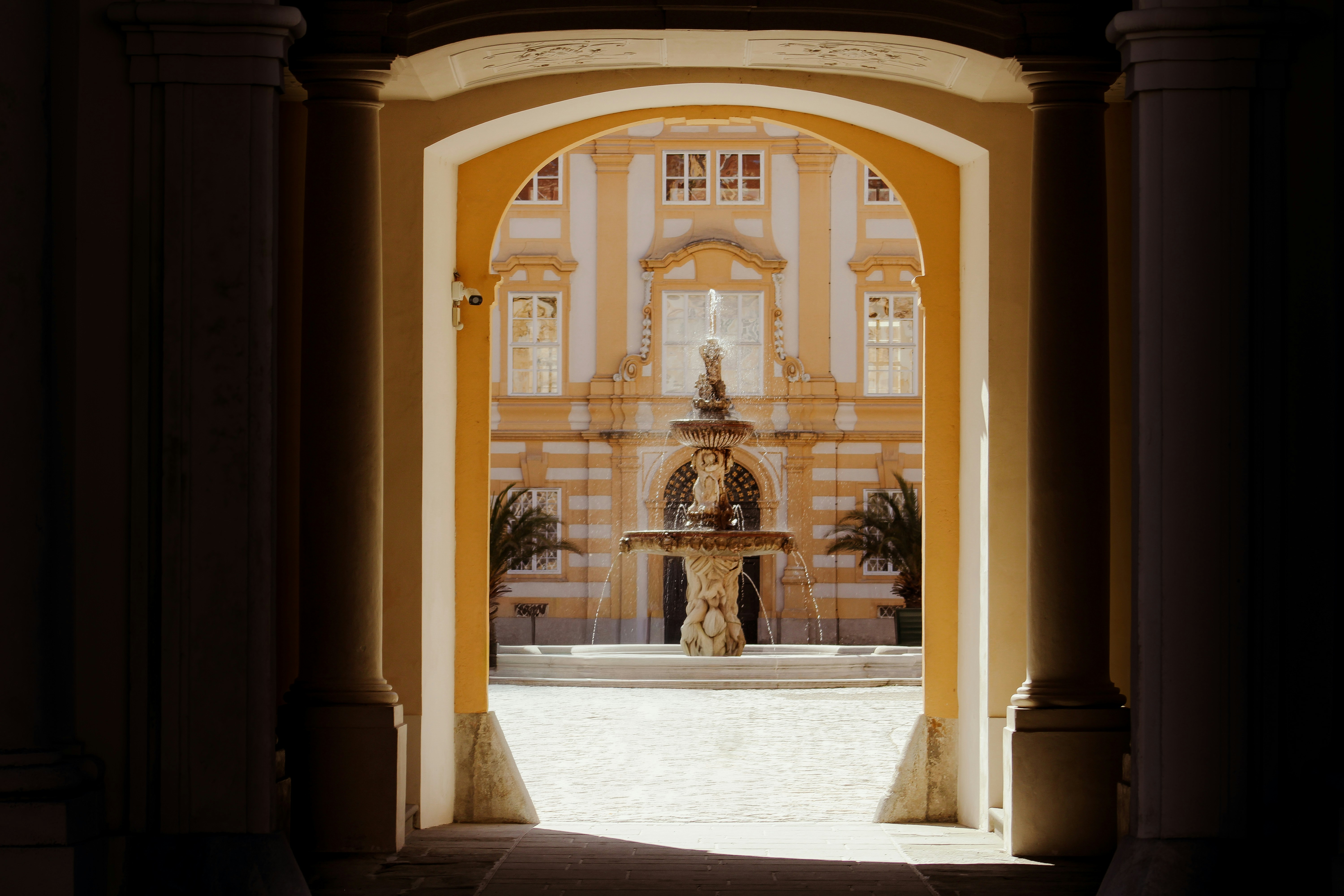 Sunlit Archway Frames a Faintly Revealed Courtyard Fountain