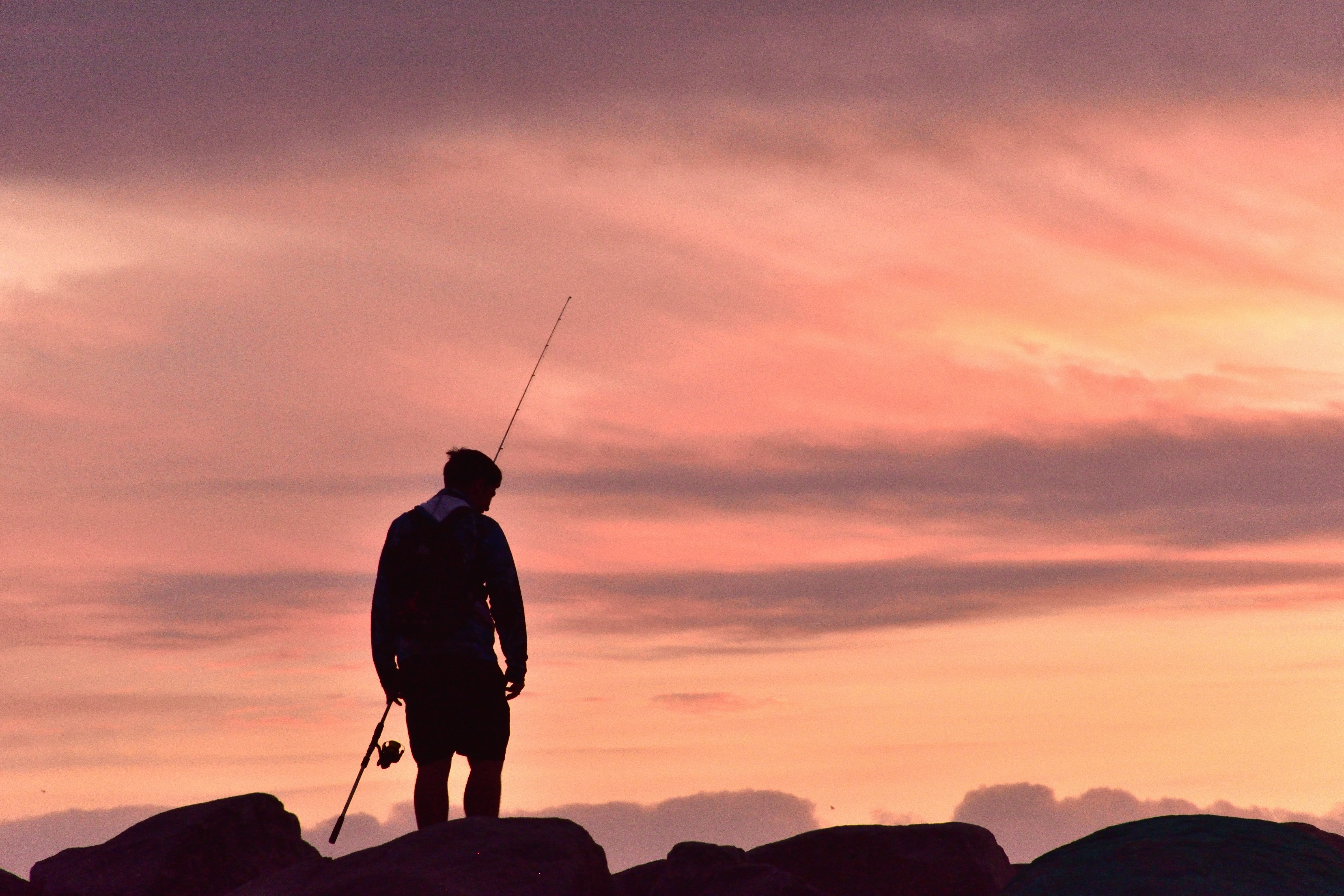 Silhouette of a lone angler at sunset on rugged shoreline