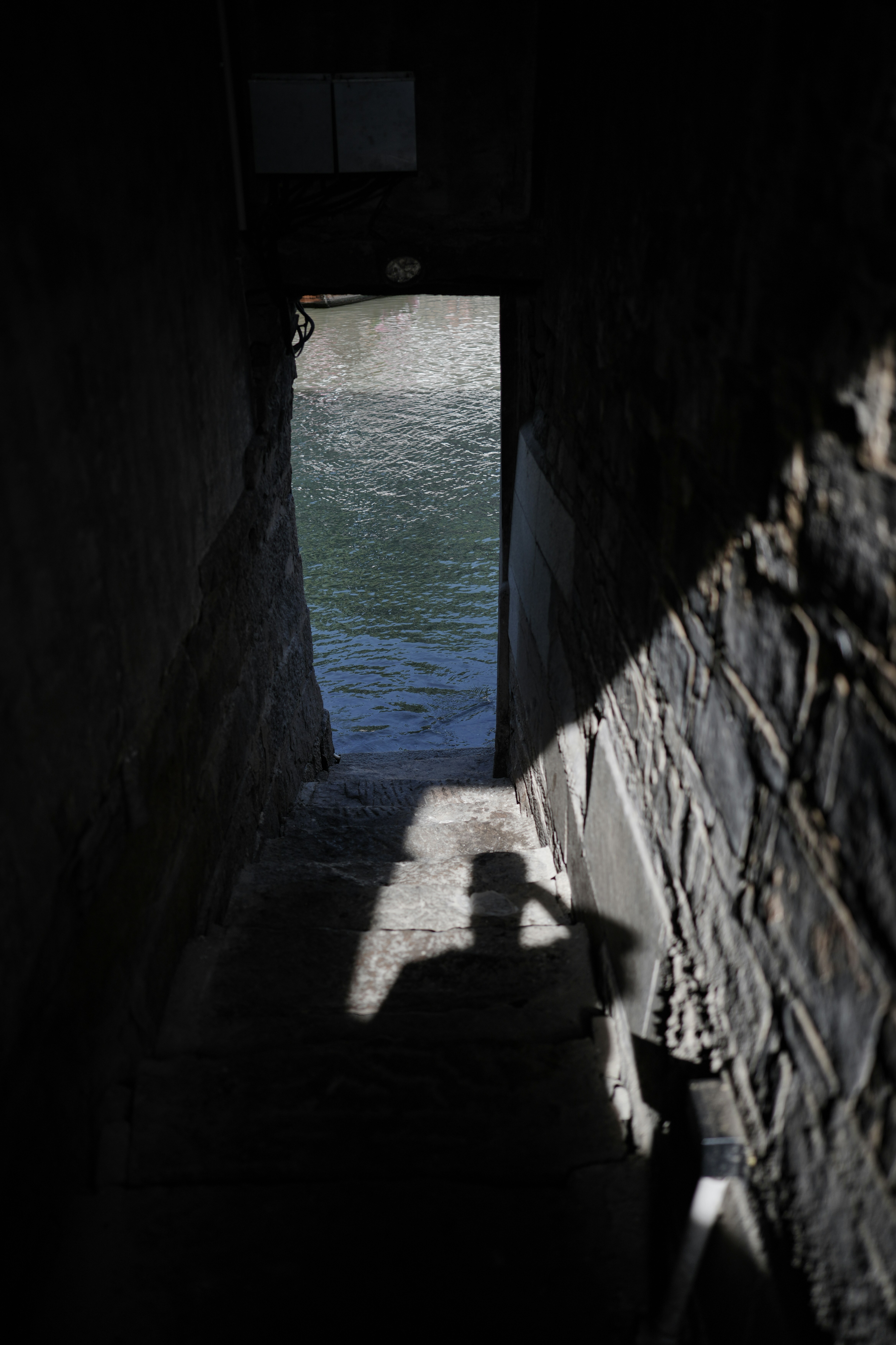 Shadowed Descent to Light: A Narrow Staircase Framing a Distant Surfaced Exit