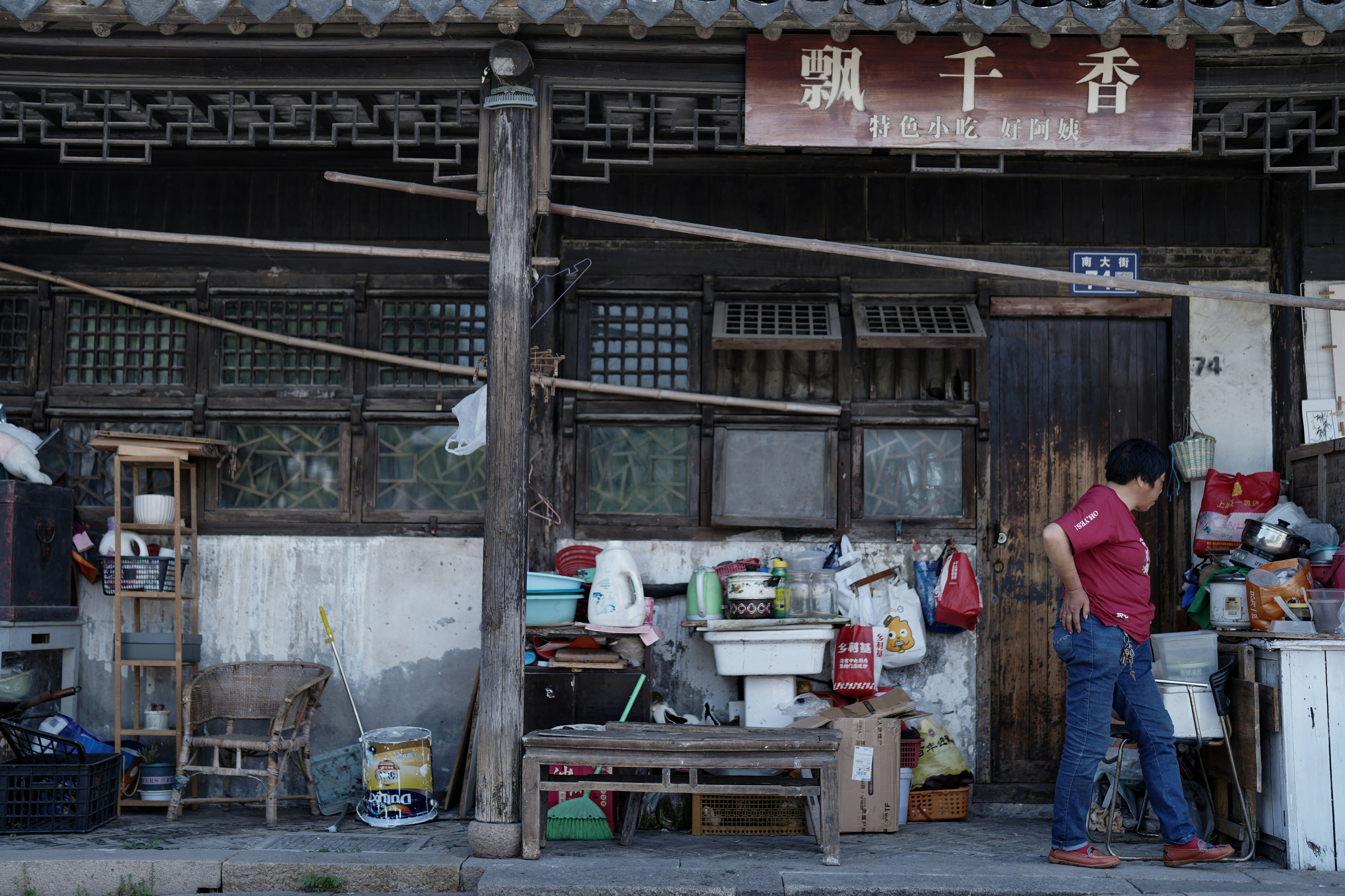 Man in a maroon shirt browses a cluttered shopfront under a weathered façade