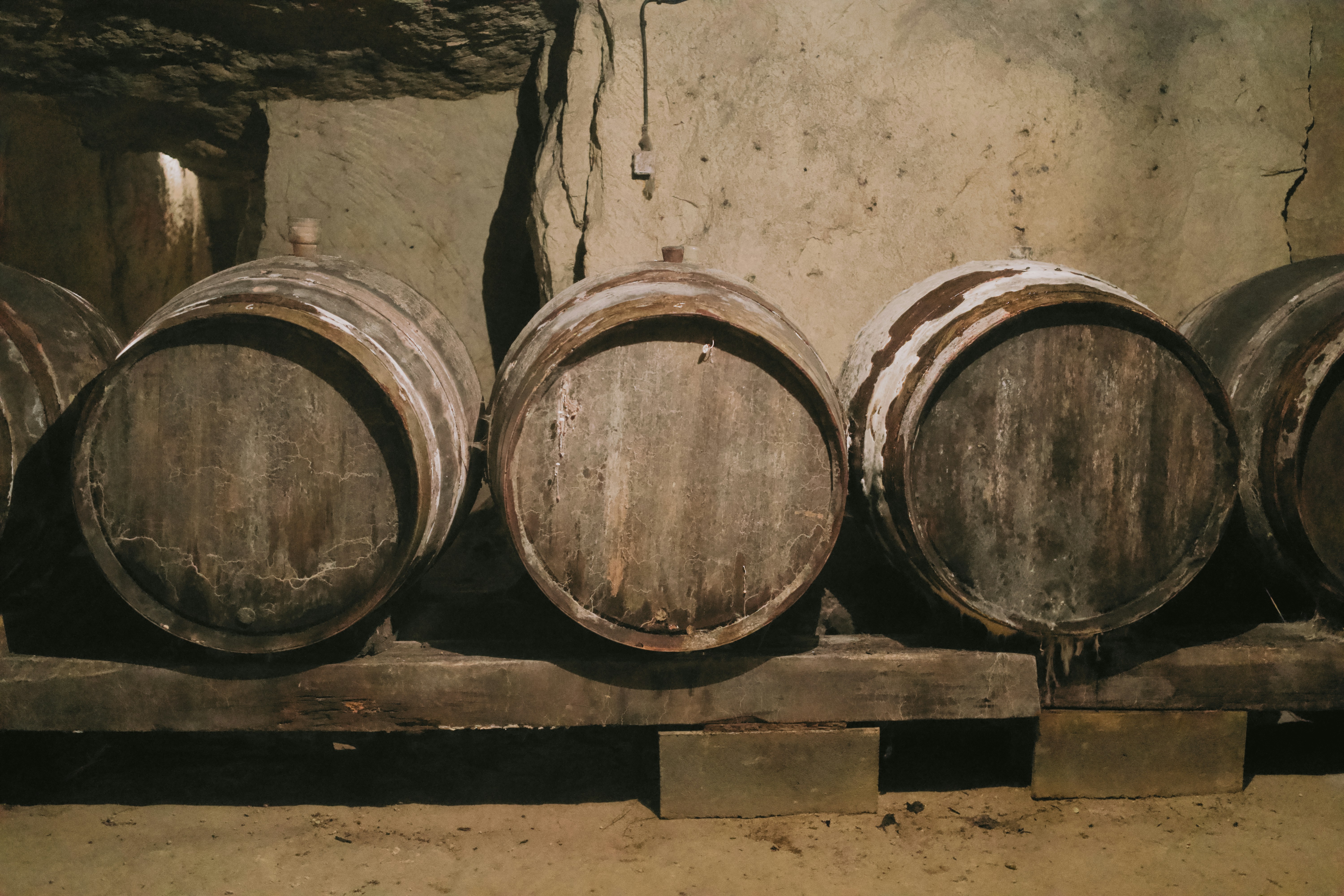 Weathered Barrels Resting on Wooden Stands in a Dim Cellar
