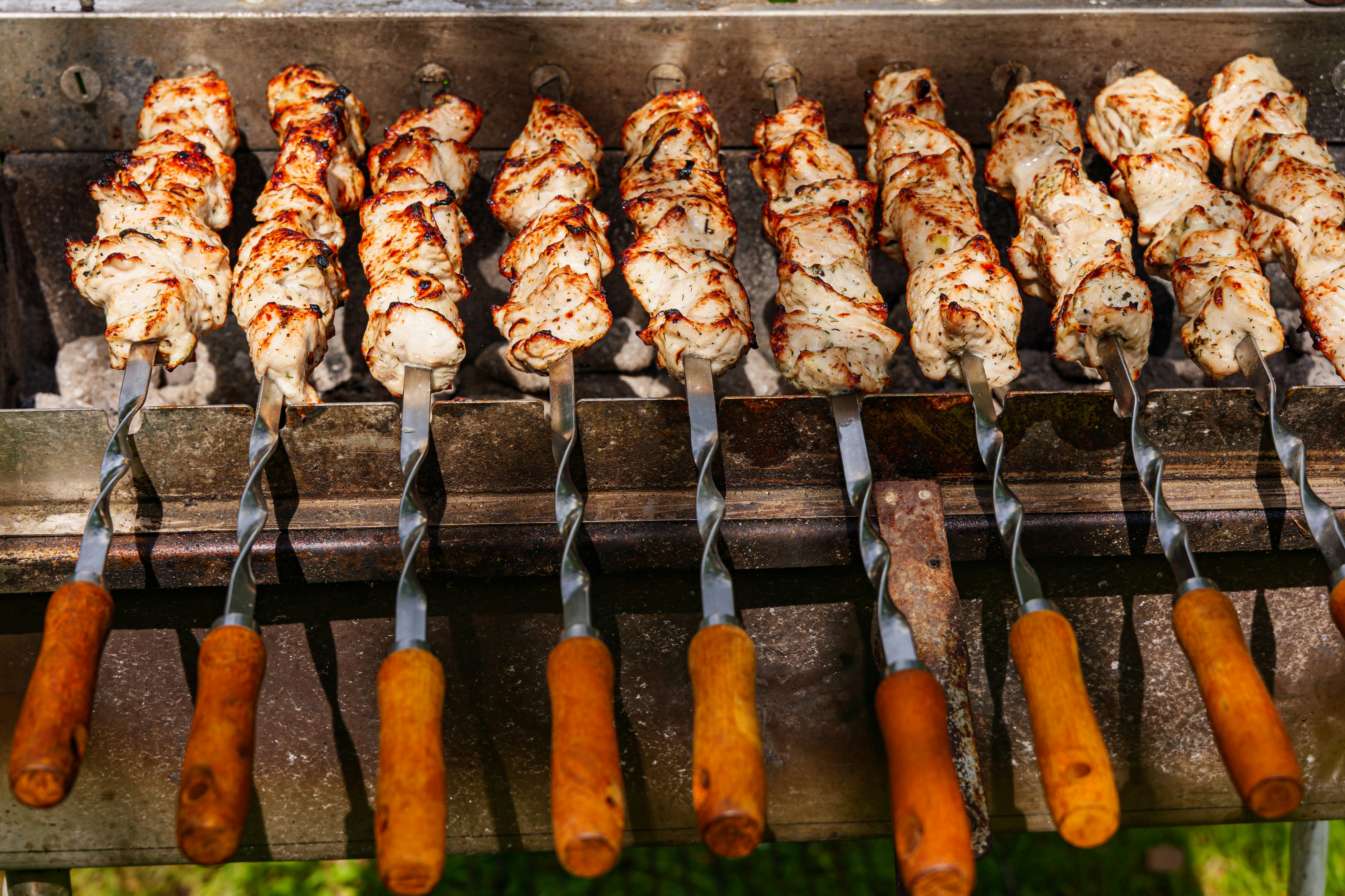 Skewers of grilled meat over a charcoal grill with wooden-handled skewers, close-up of the sizzling barbecue setup.