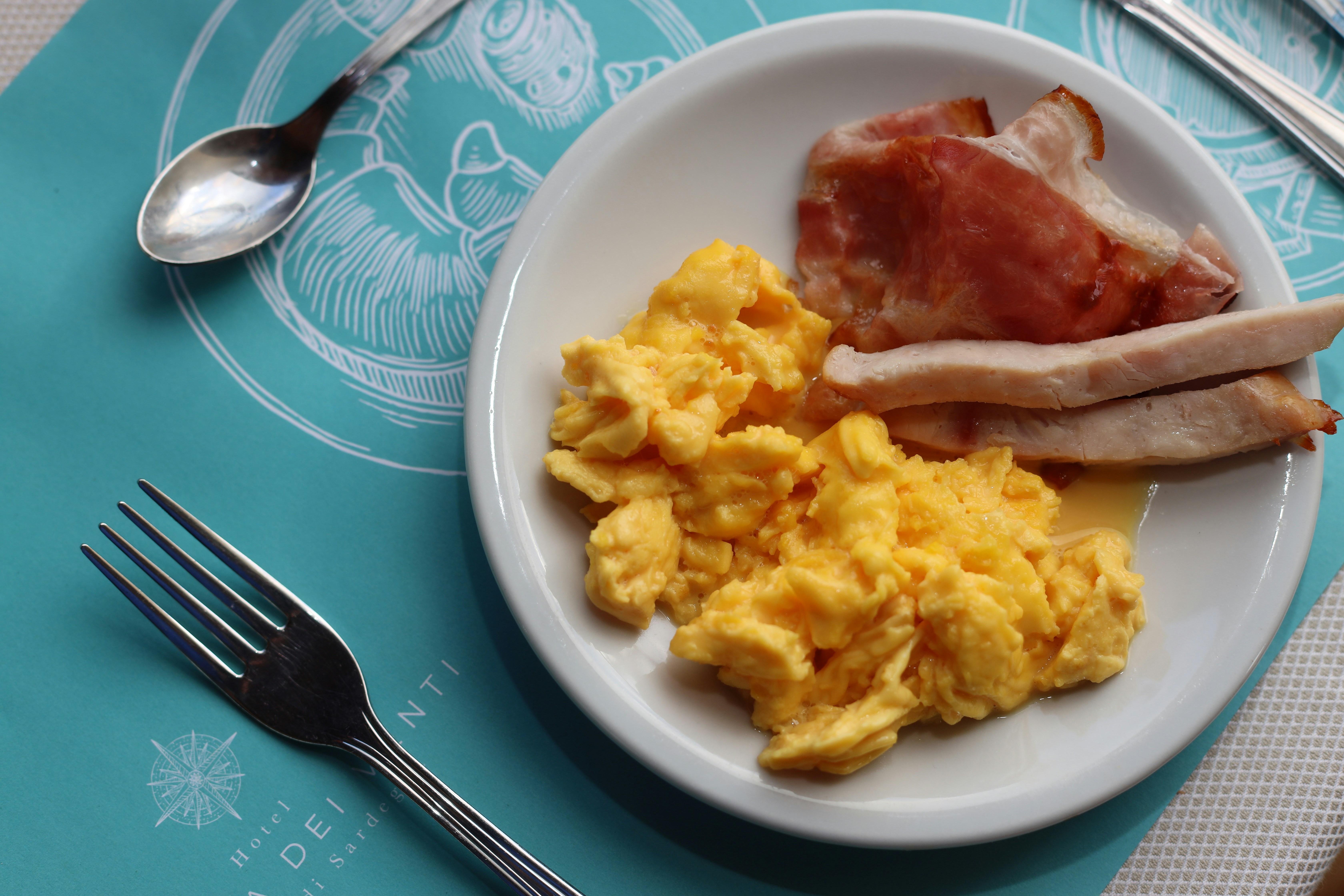 Plate of scrambled eggs with bacon on a teal placemat