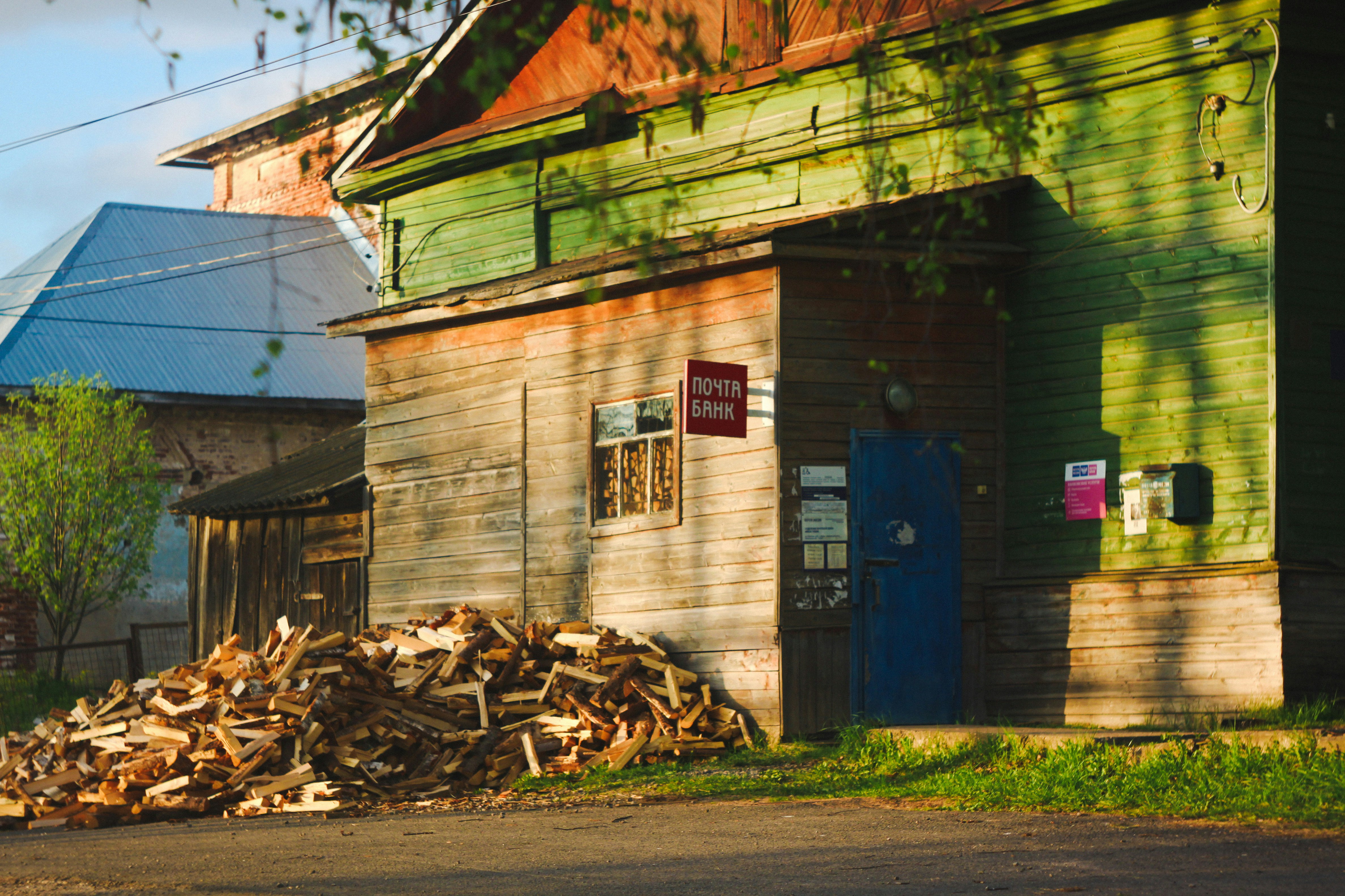 Sunlit Bankfront with Firewood Pile and Weathered Green Facade