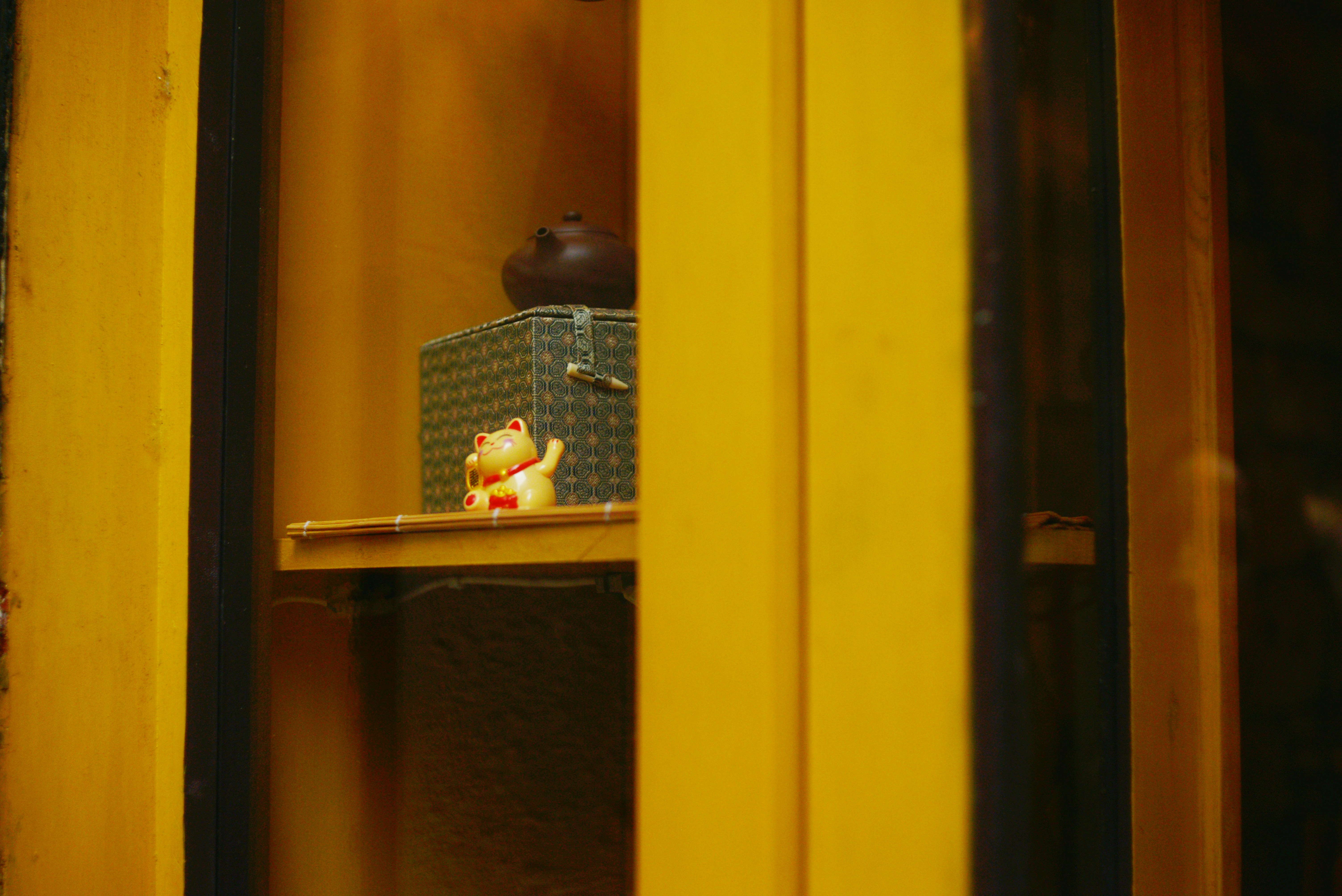 Maneki-neko on a shelf behind yellow window frames