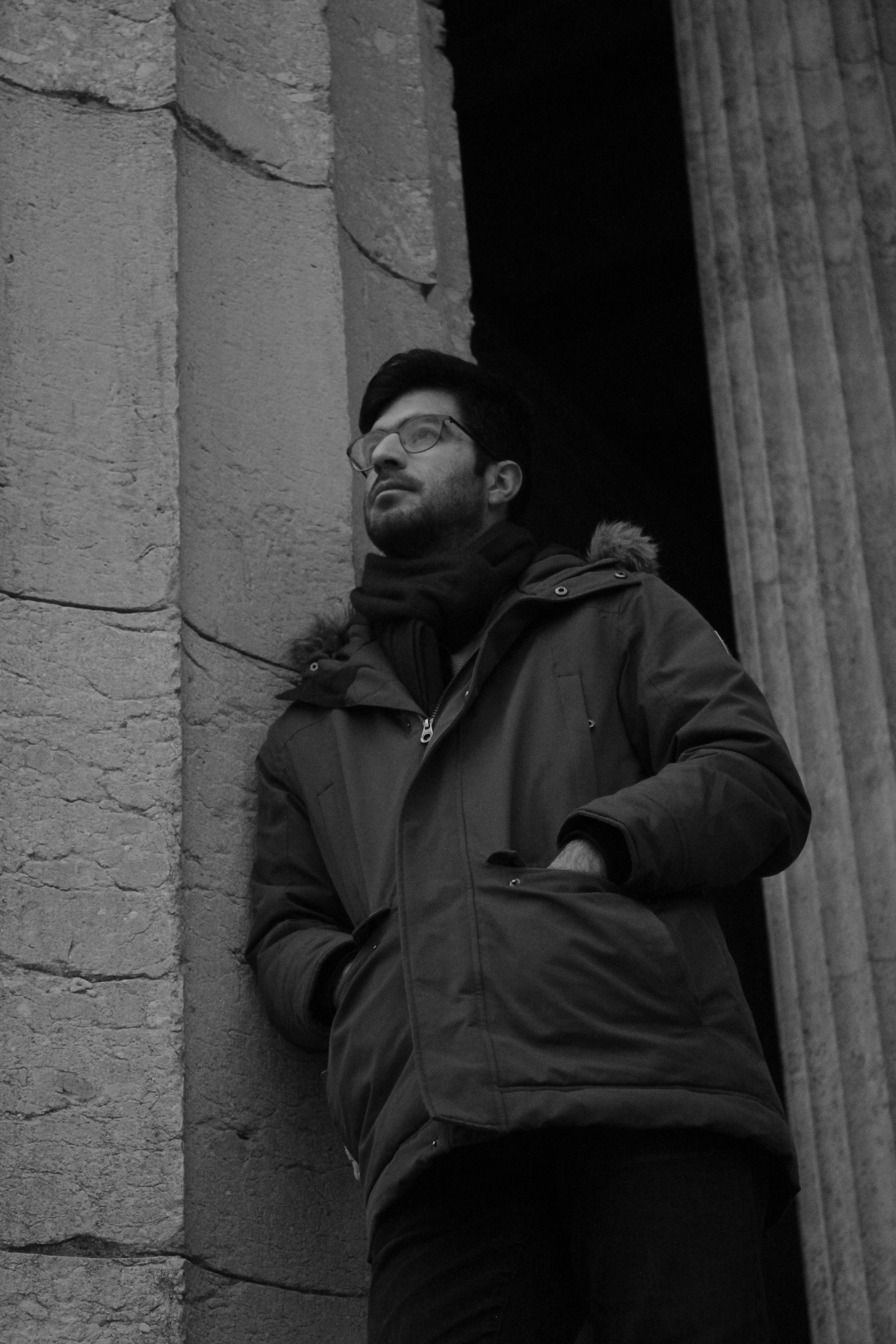 Man in a winter coat leans into a stone doorway at dusk