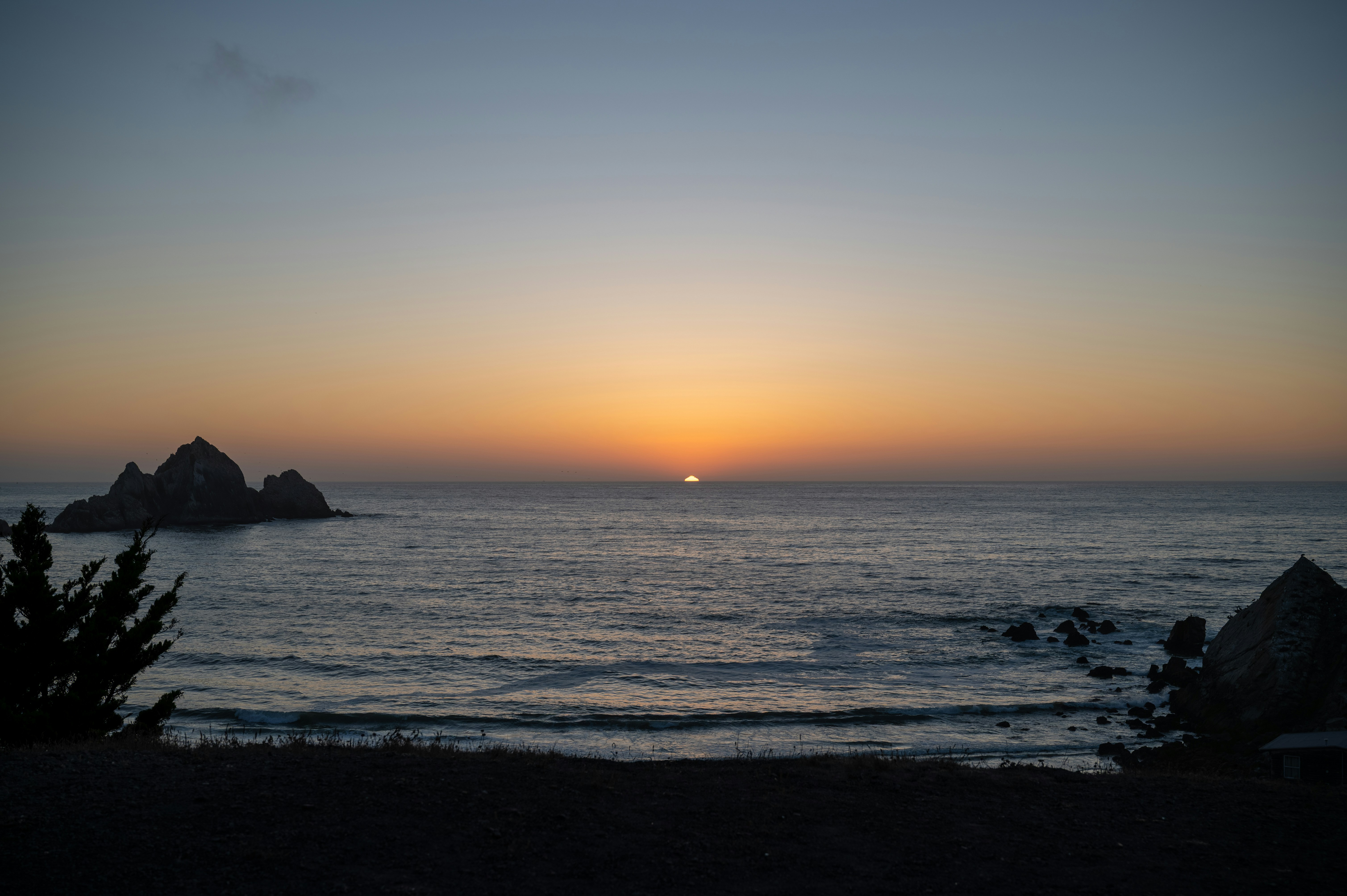 Sun slipping into the horizon over a tranquil coastal silhouette