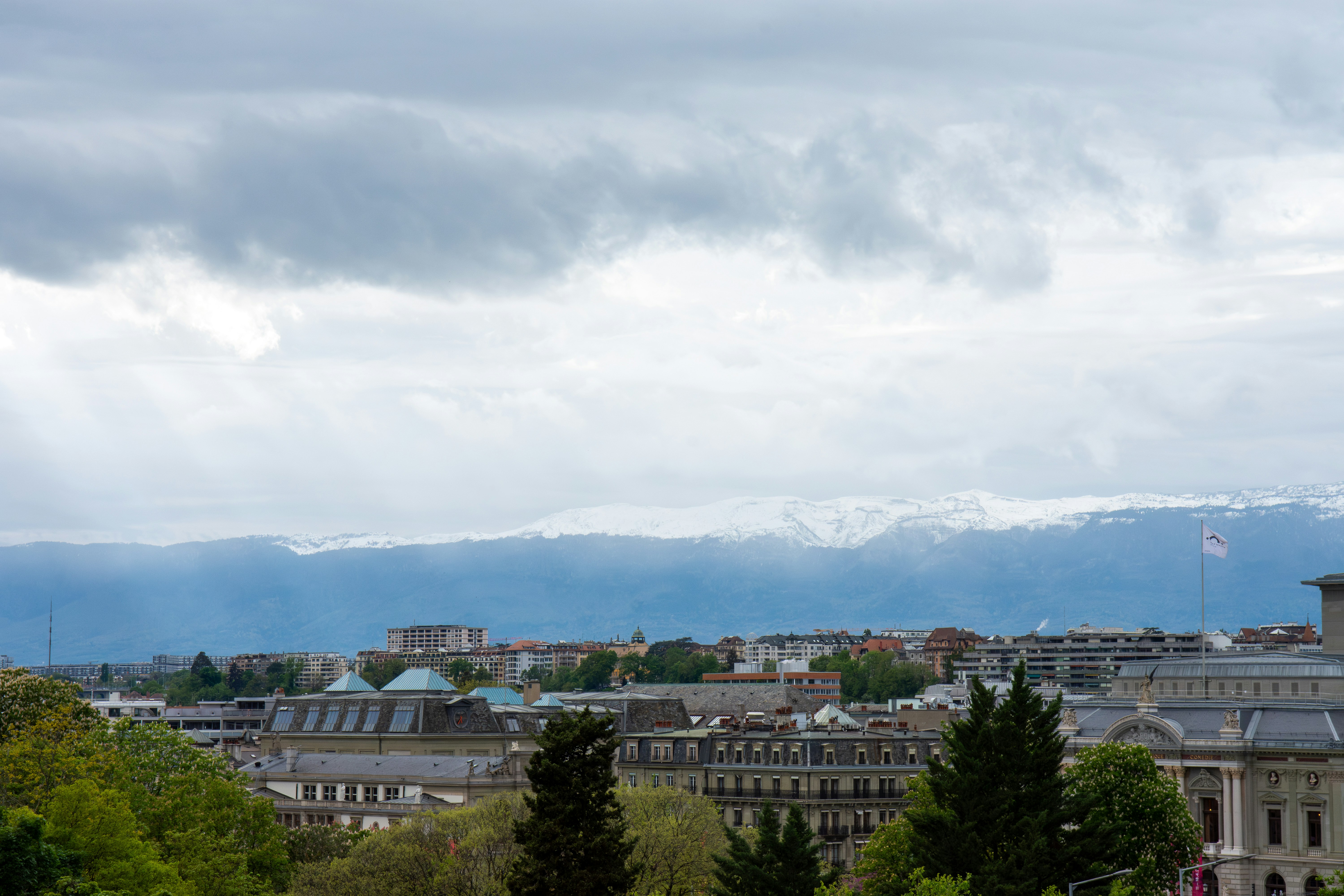 Urban panorama beneath a stormy sky with distant alpine backdrop