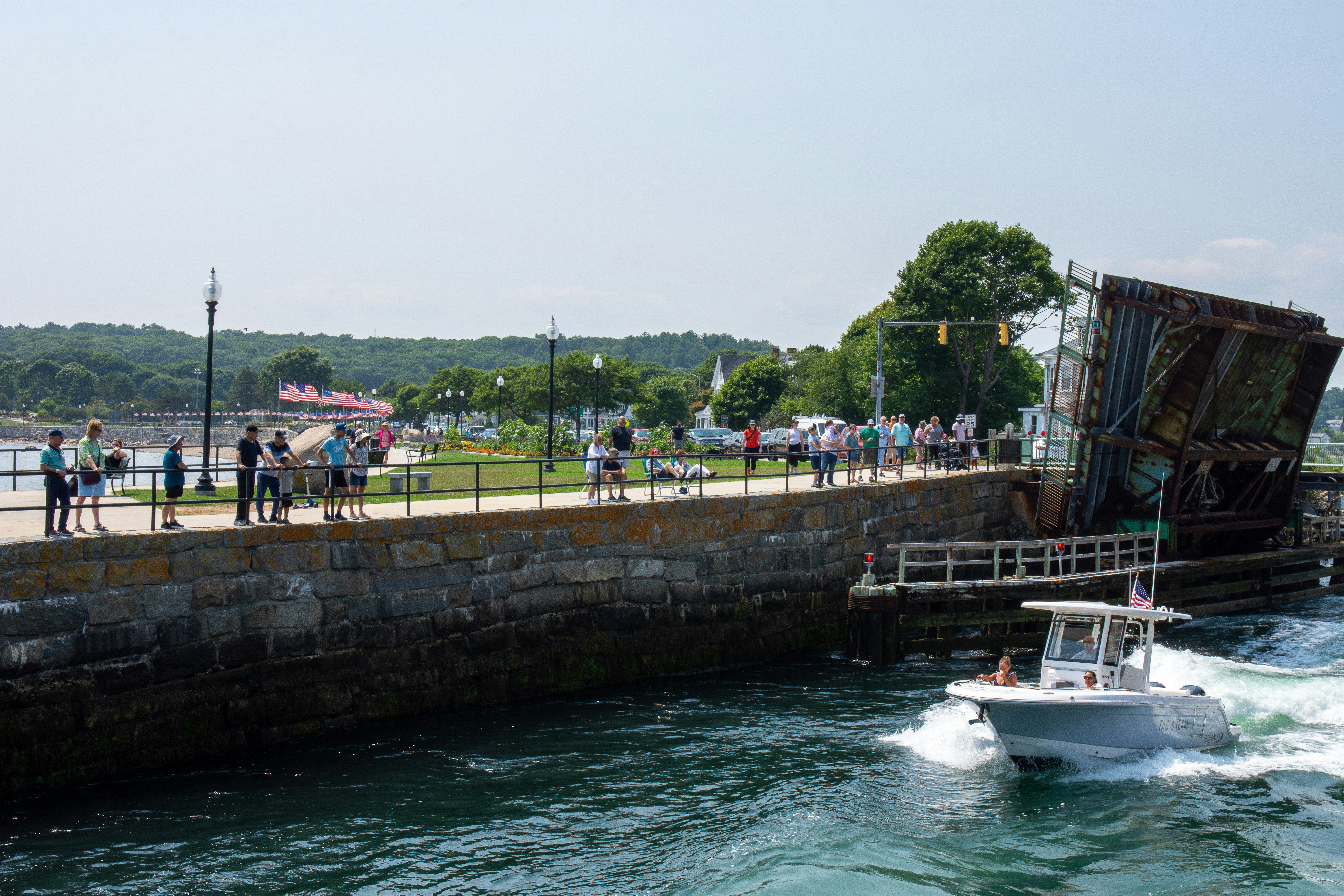 Crowd on the seawall watches a speedboat emerge from a docked gate