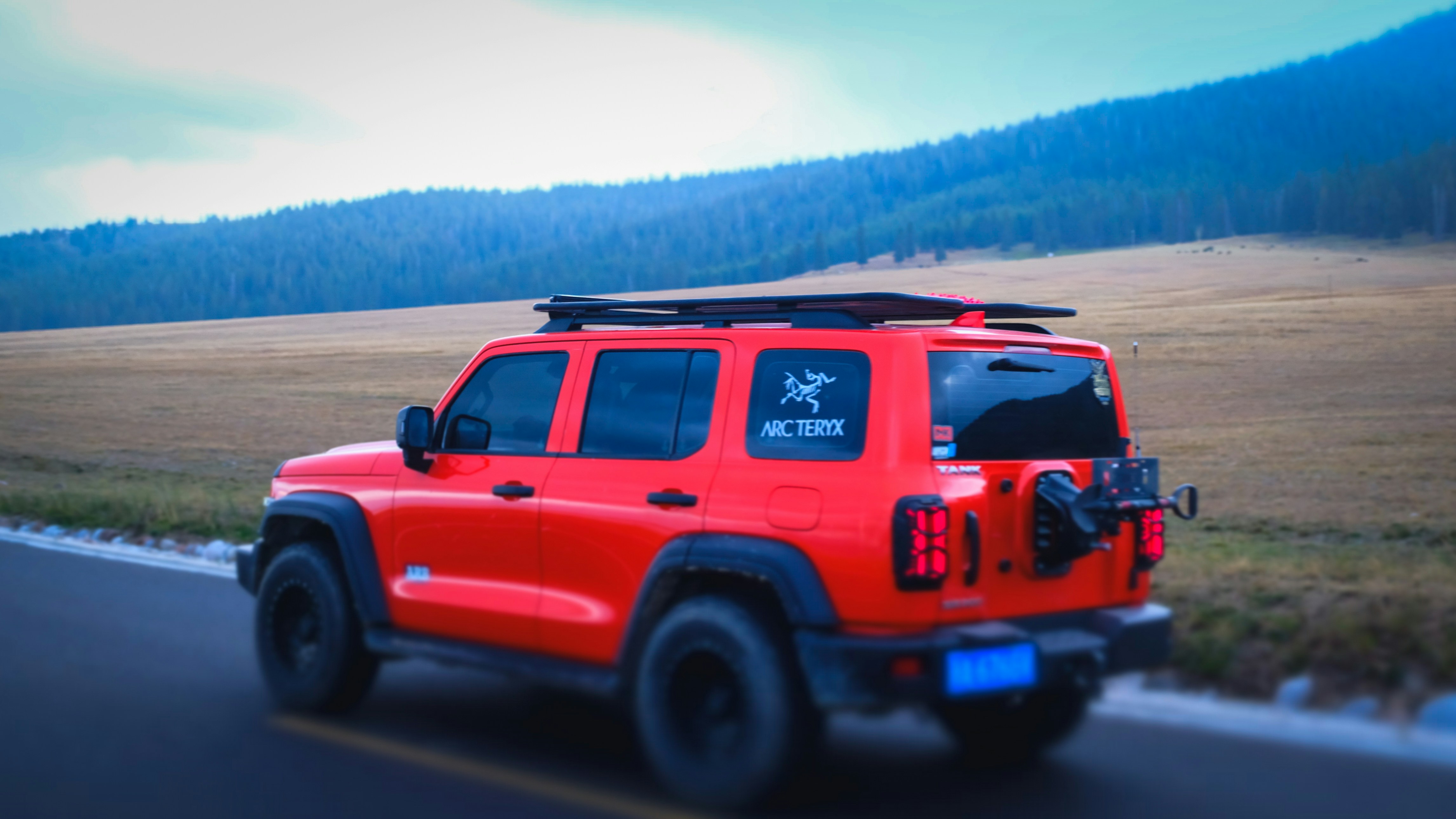 Red Adventure SUV in Motion: Fields, Sky, and Distant Hills