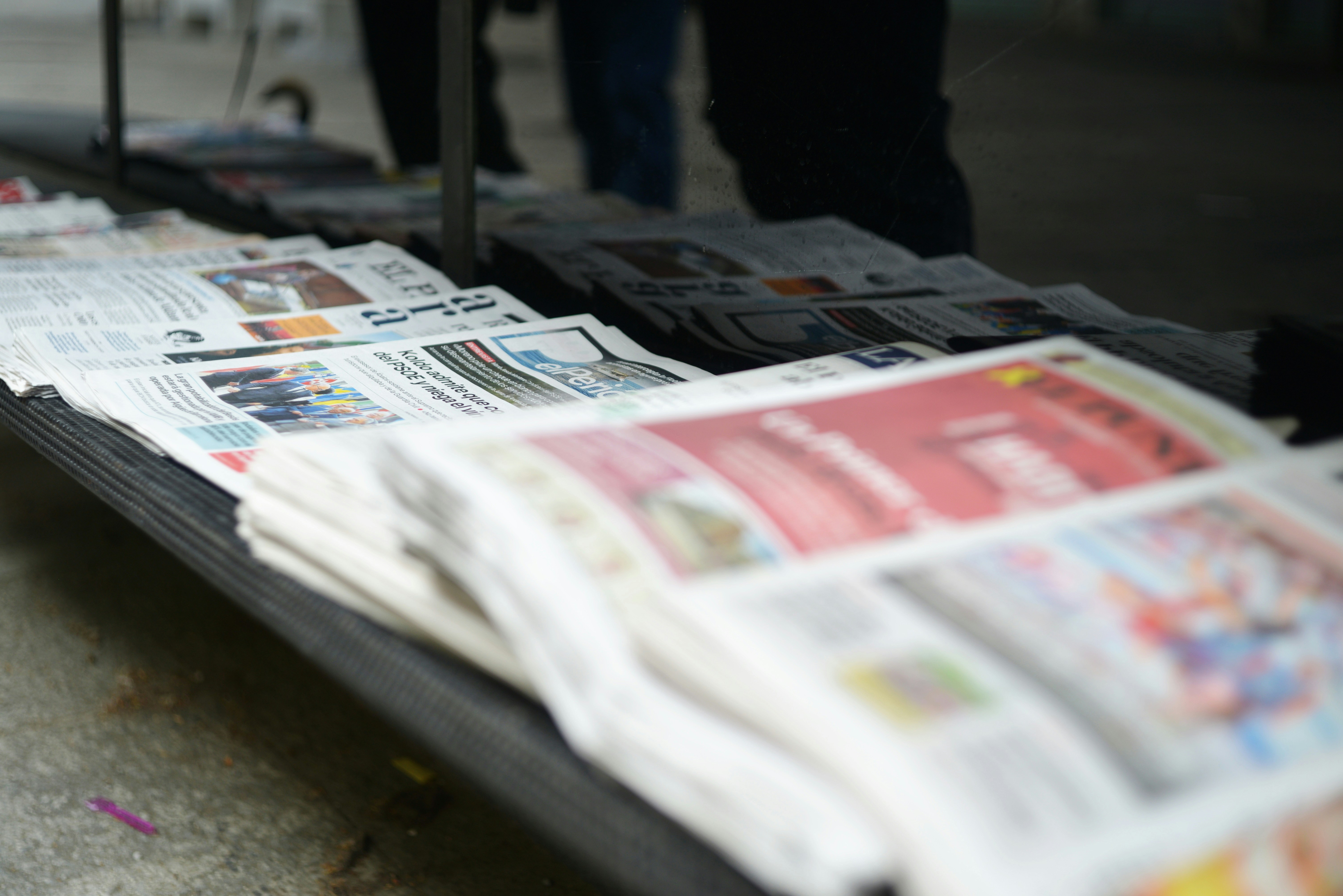 Newspaper Stall in Blur: Street Papers Fanned Across a Taint of Concrete