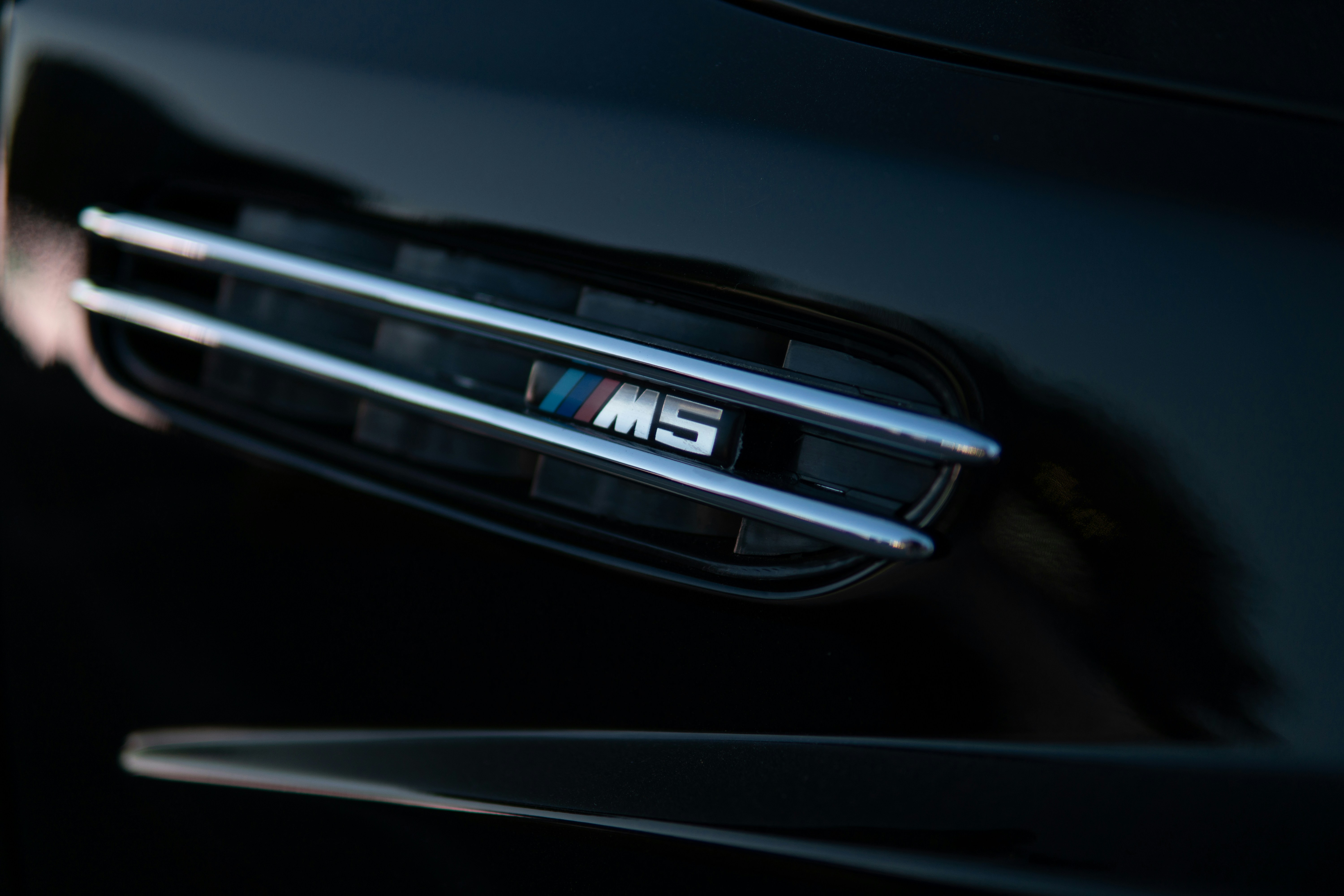 Midnight M Badge: A Close-Up of BMW M5 Emblem in Dim Reflection