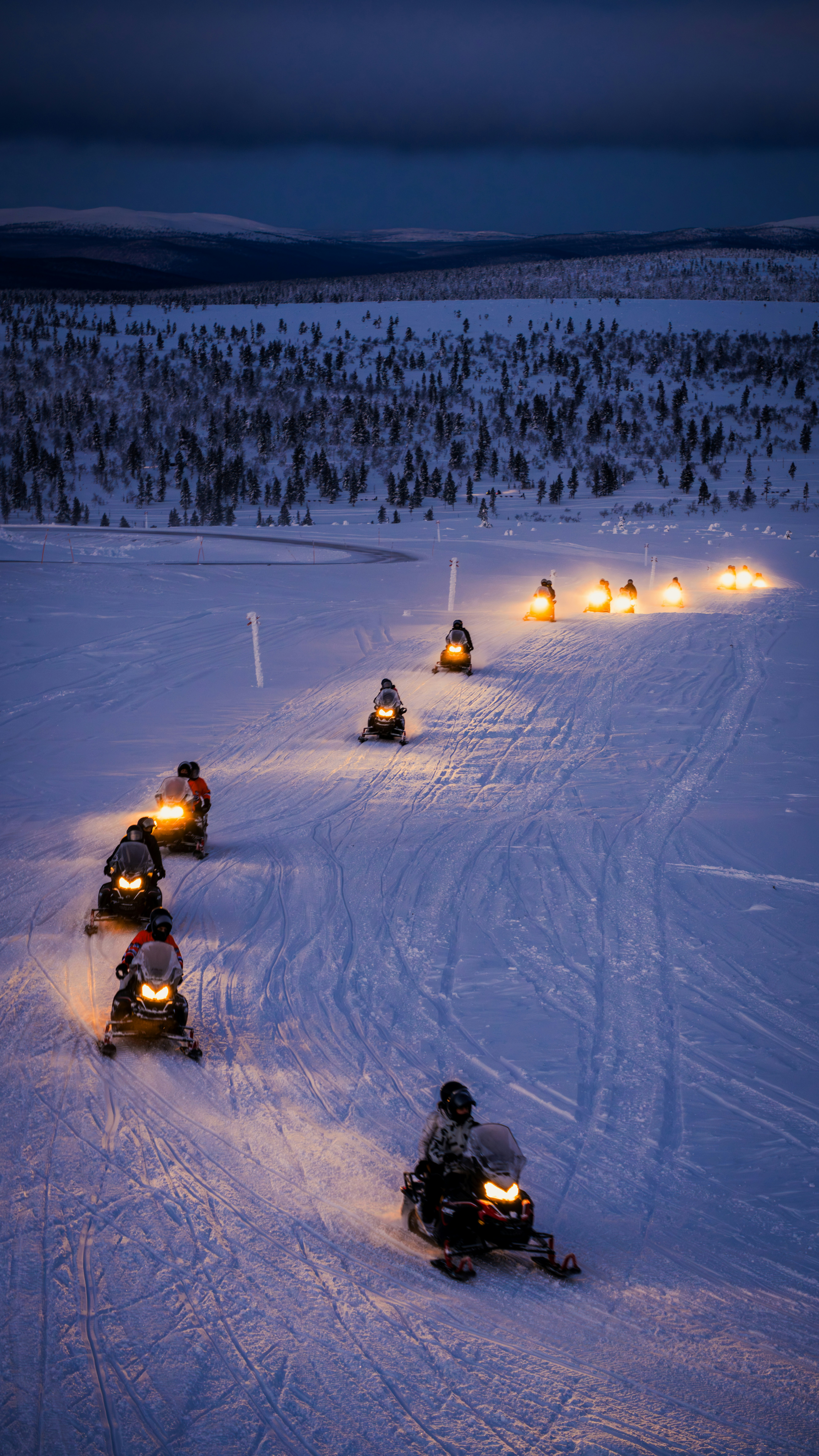 Snowmobiles with bright headlights traverse a dark, snowy winter ...
