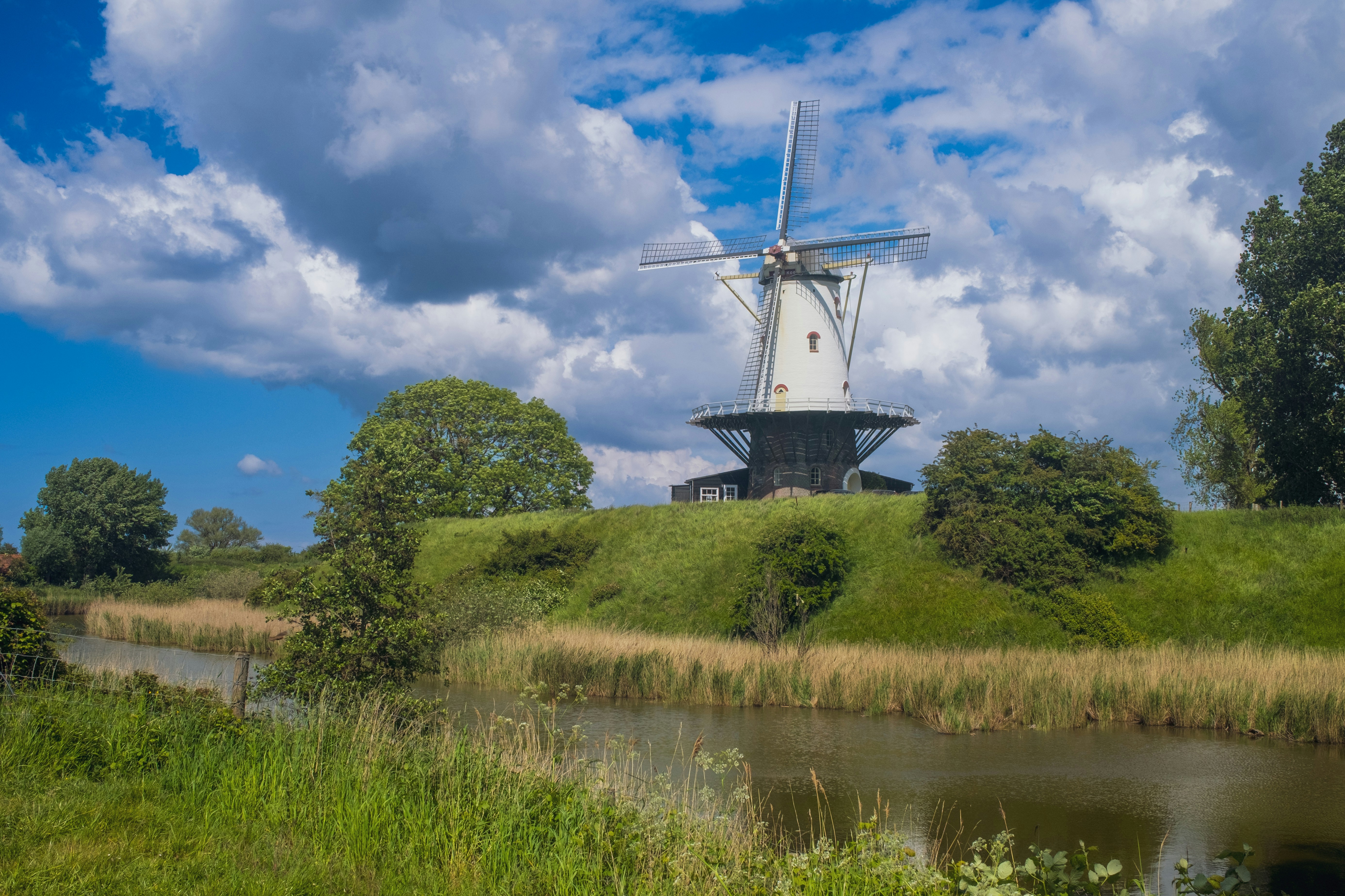 Windmill on the grassy riverbank under a blue sky