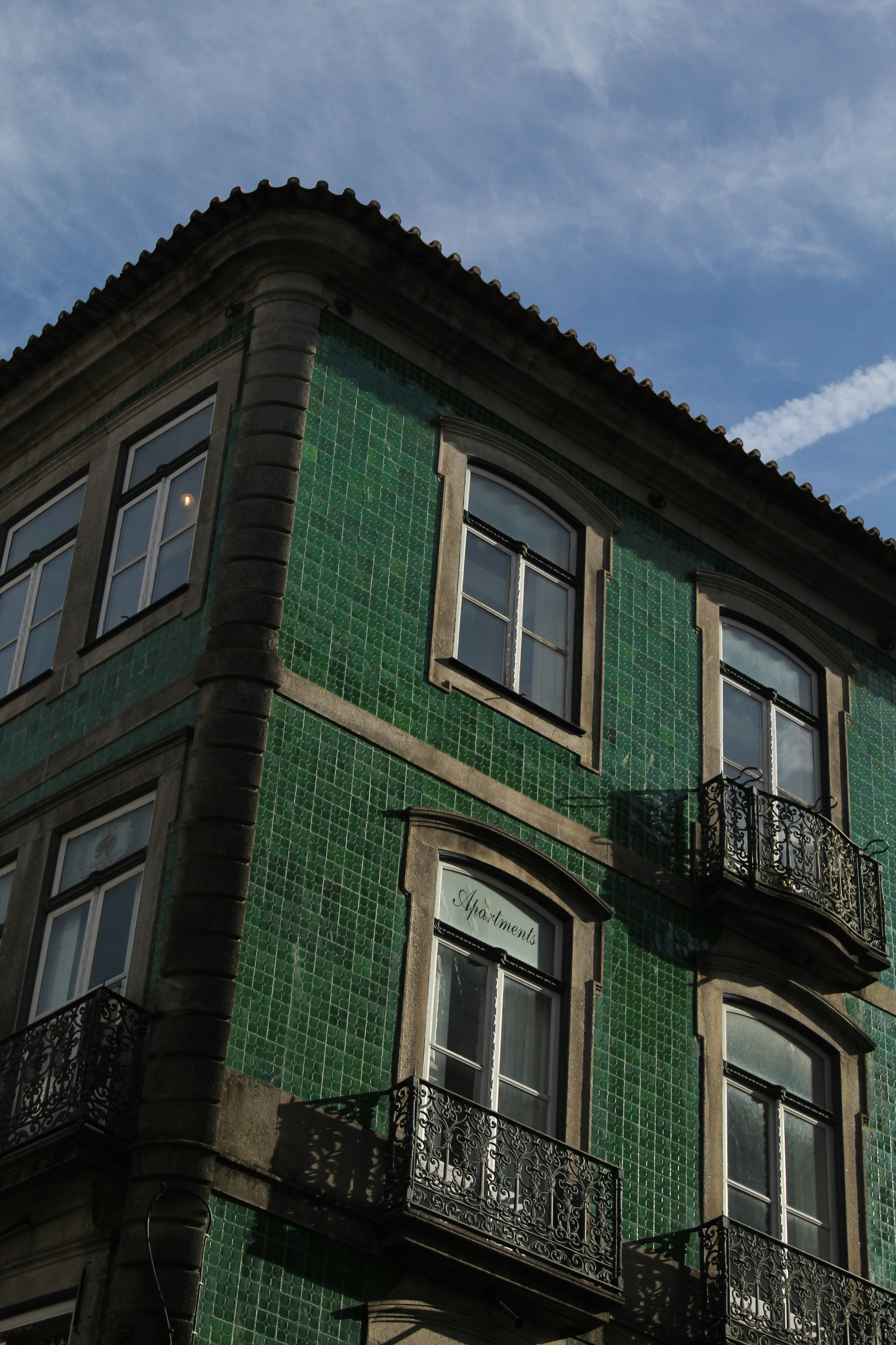 Green tiled facade under a sky: corner of a historic building with wrought-iron balconies