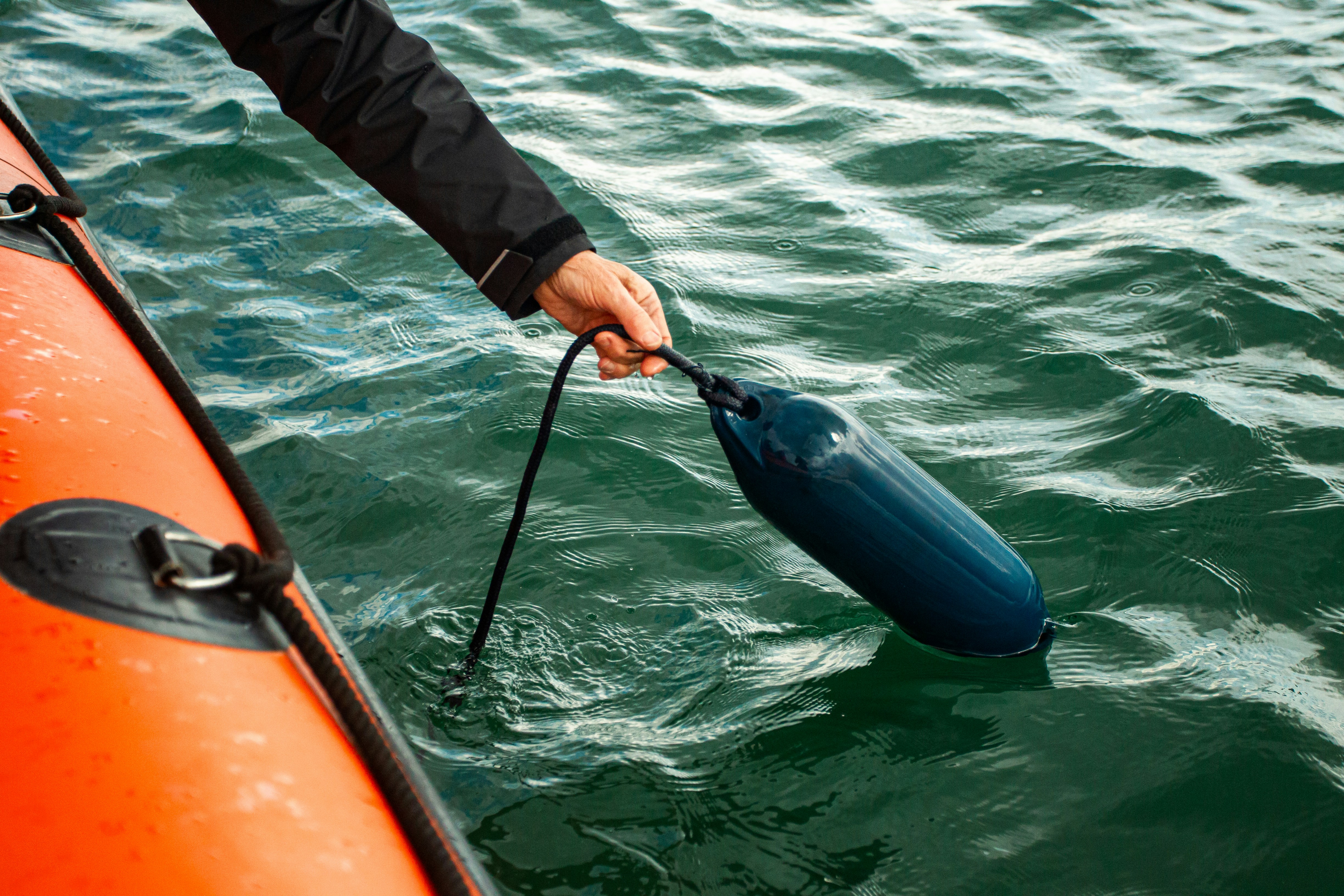Hand Reeling a Blue Buoy Near a Red Inflatable Boat