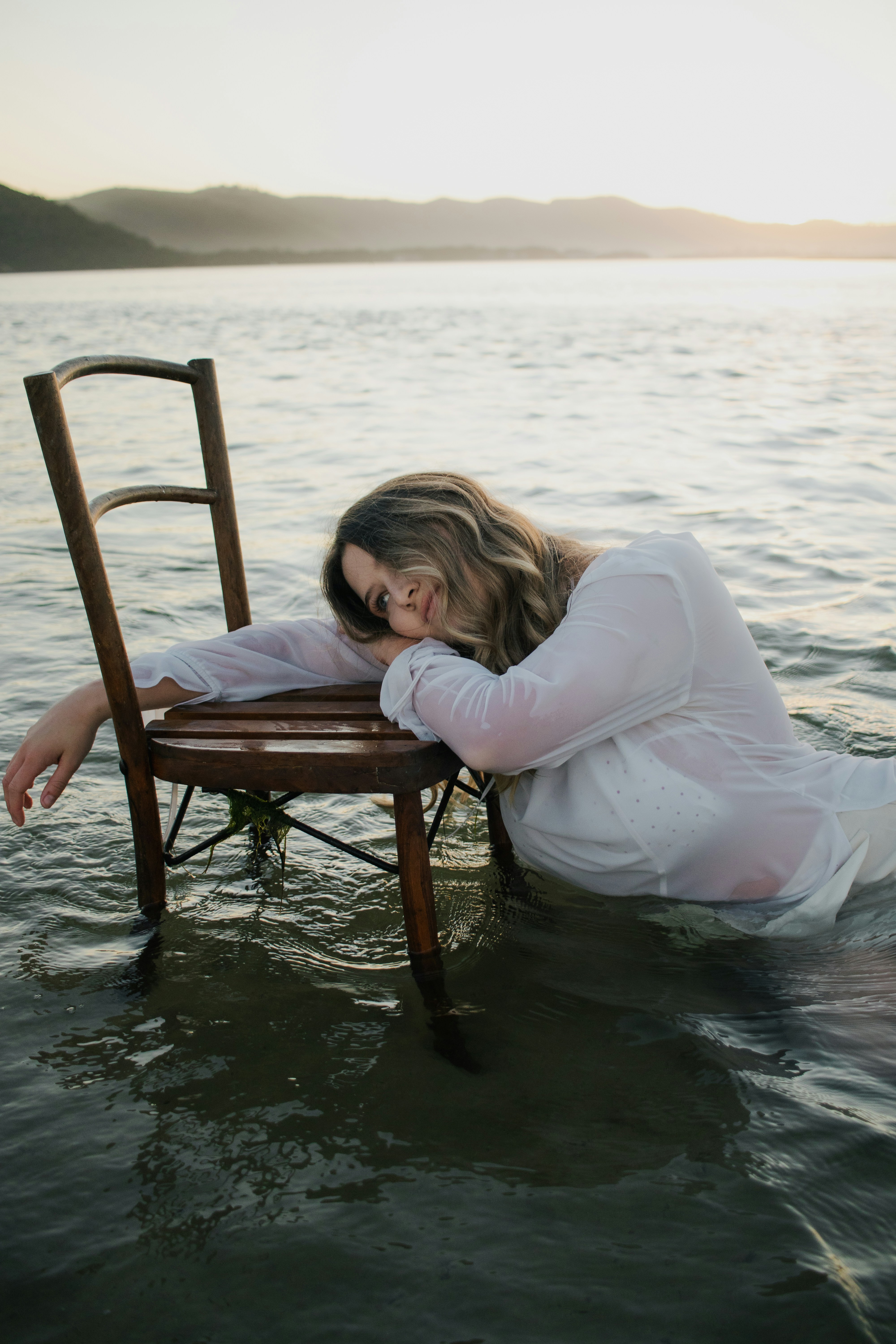 Resting by the Shore: A Woman Leaning on a Wooden Chair in Quiet Sunset Waters