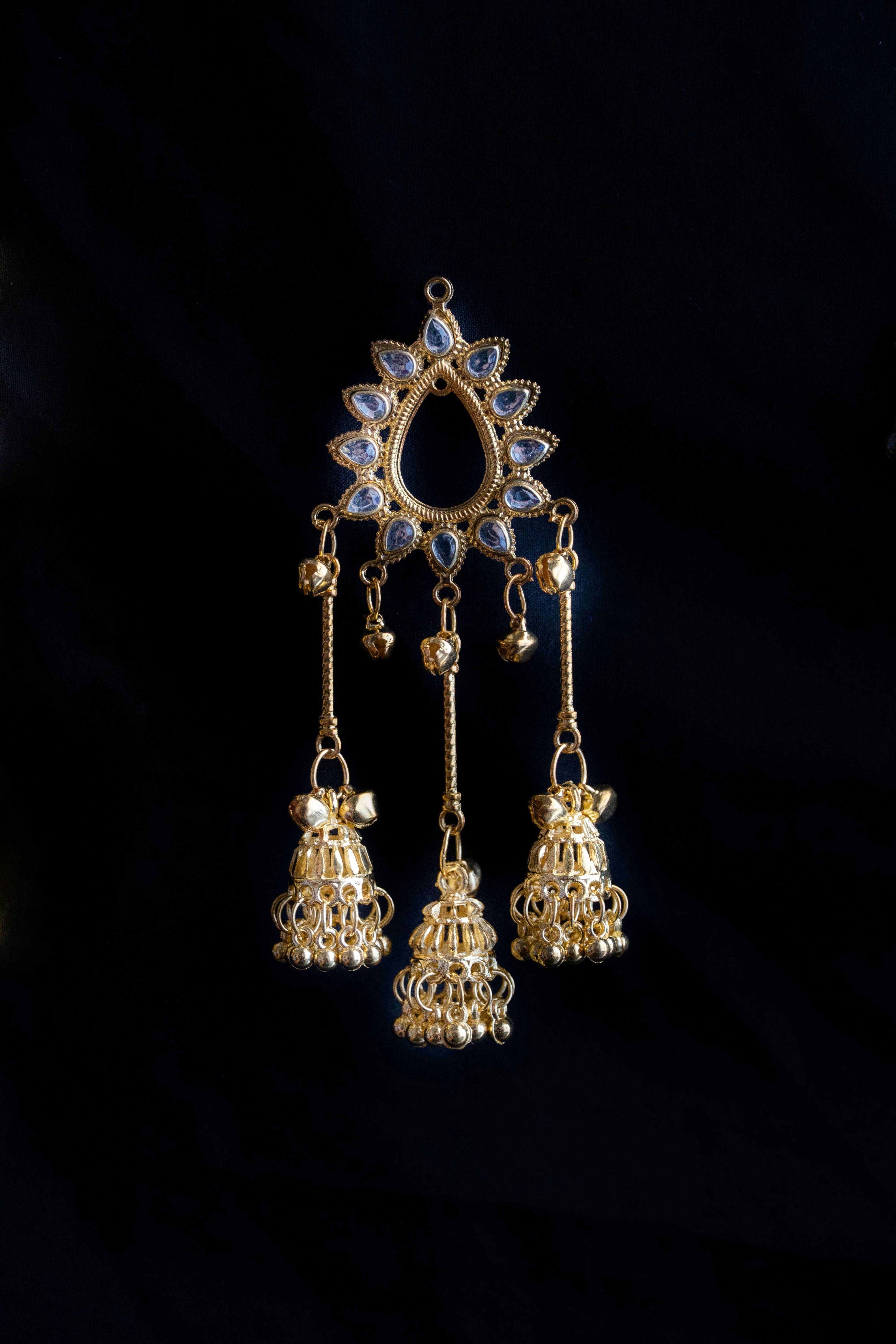 Ornate gold pendant with dangling filigree bells against a velvet black backdrop