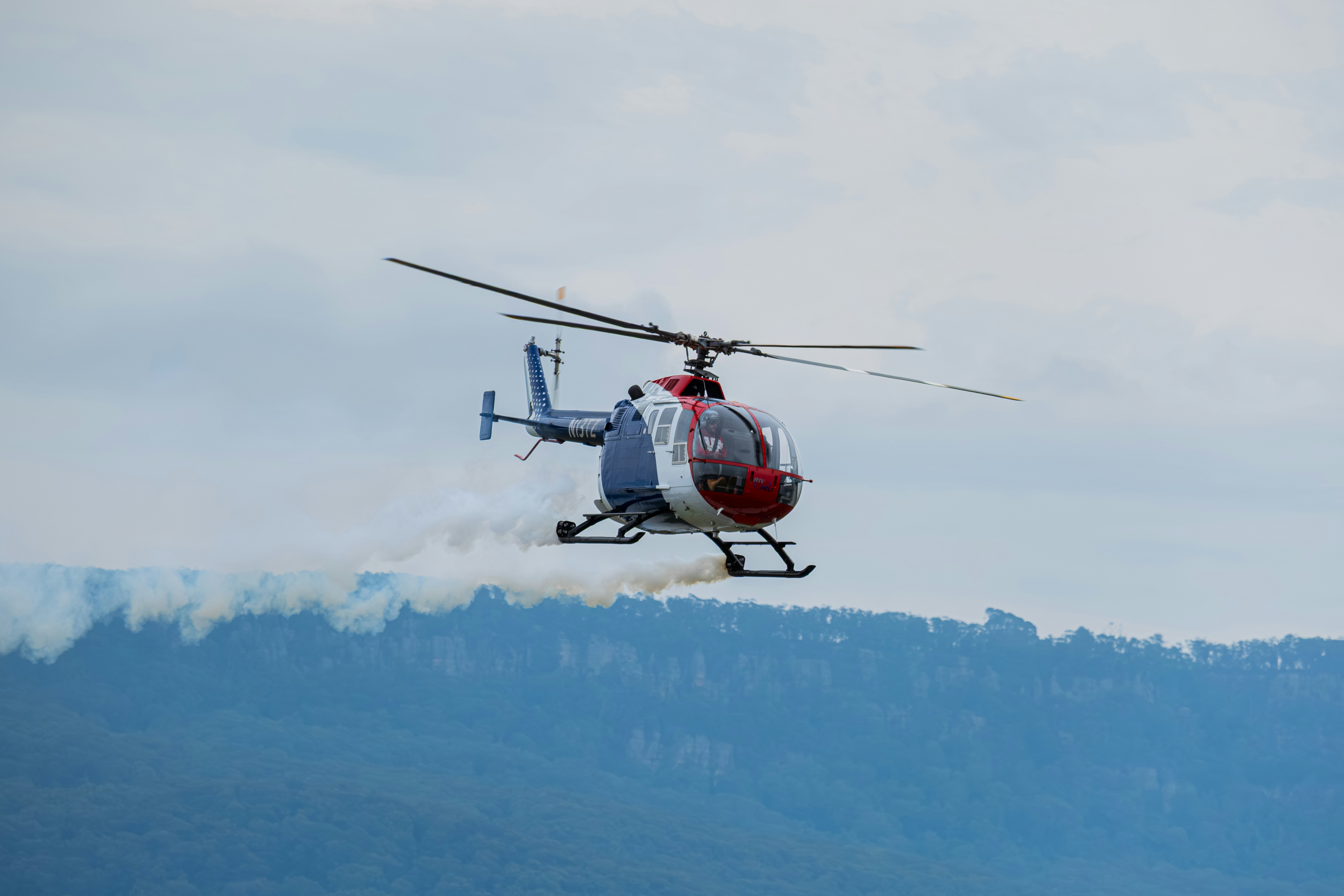 Red-and-White Rescue: Helicopter Hover over a Misty Ridge