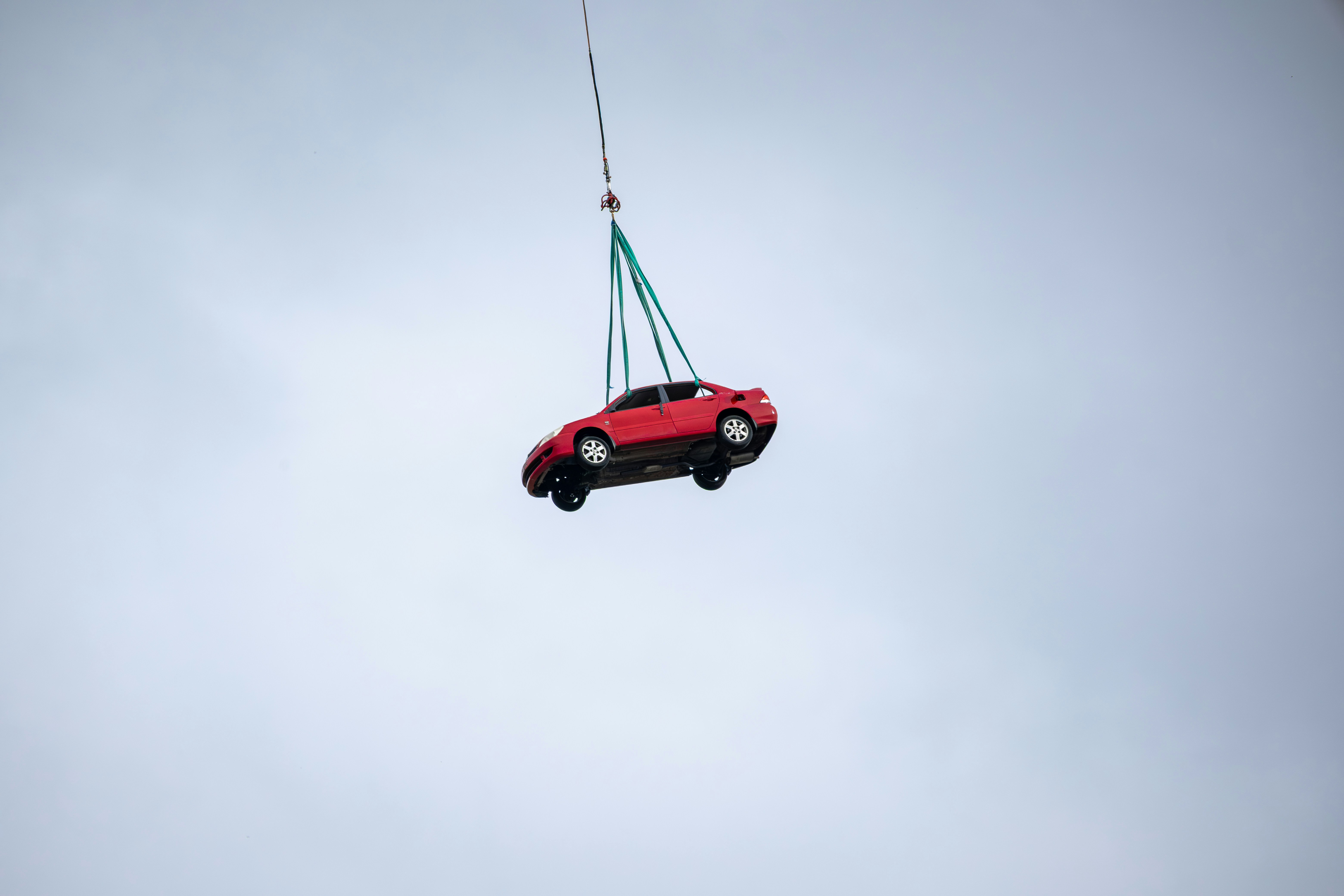 Elevated Rescue: a red car suspended mid‑air against a pale sky