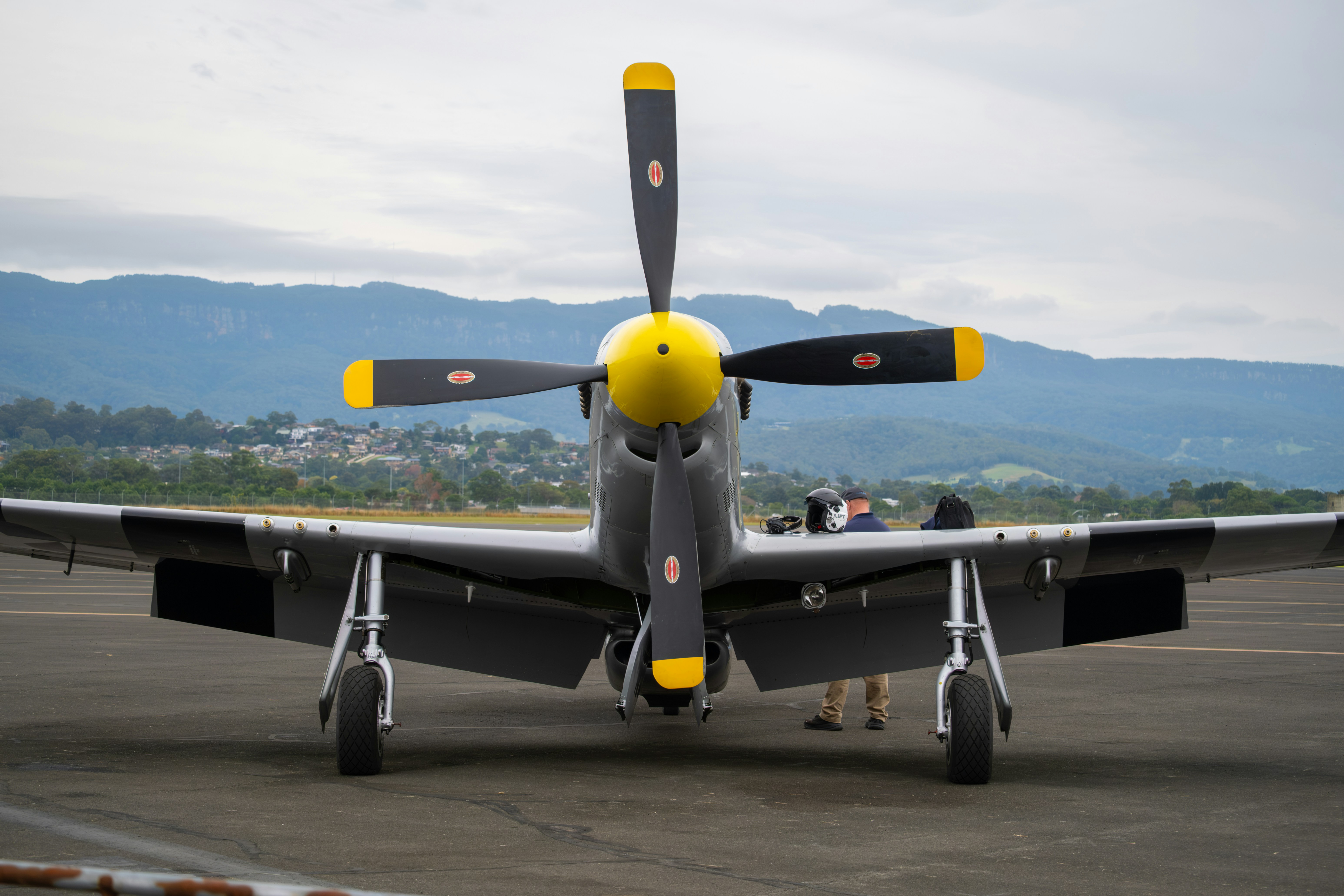 A striking front-on view of a restored North American P-51 Mustang parked on the tarmac at an airshow, showcasing its iconic four-blade propeller and sleek World War II fighter design.