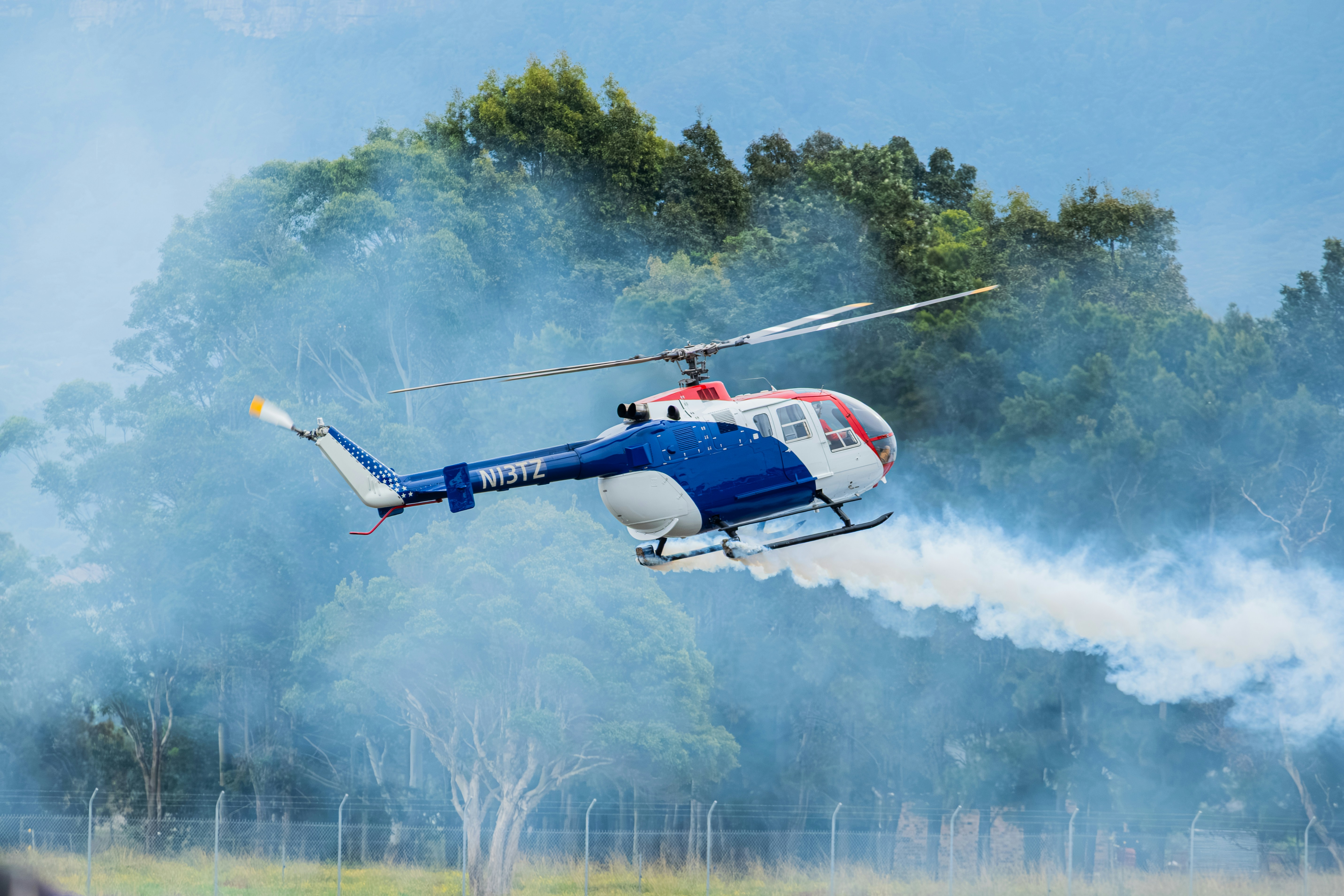 Blue-and-White Rescue Helikopter Cutting Through Smoke Over a Tree Line