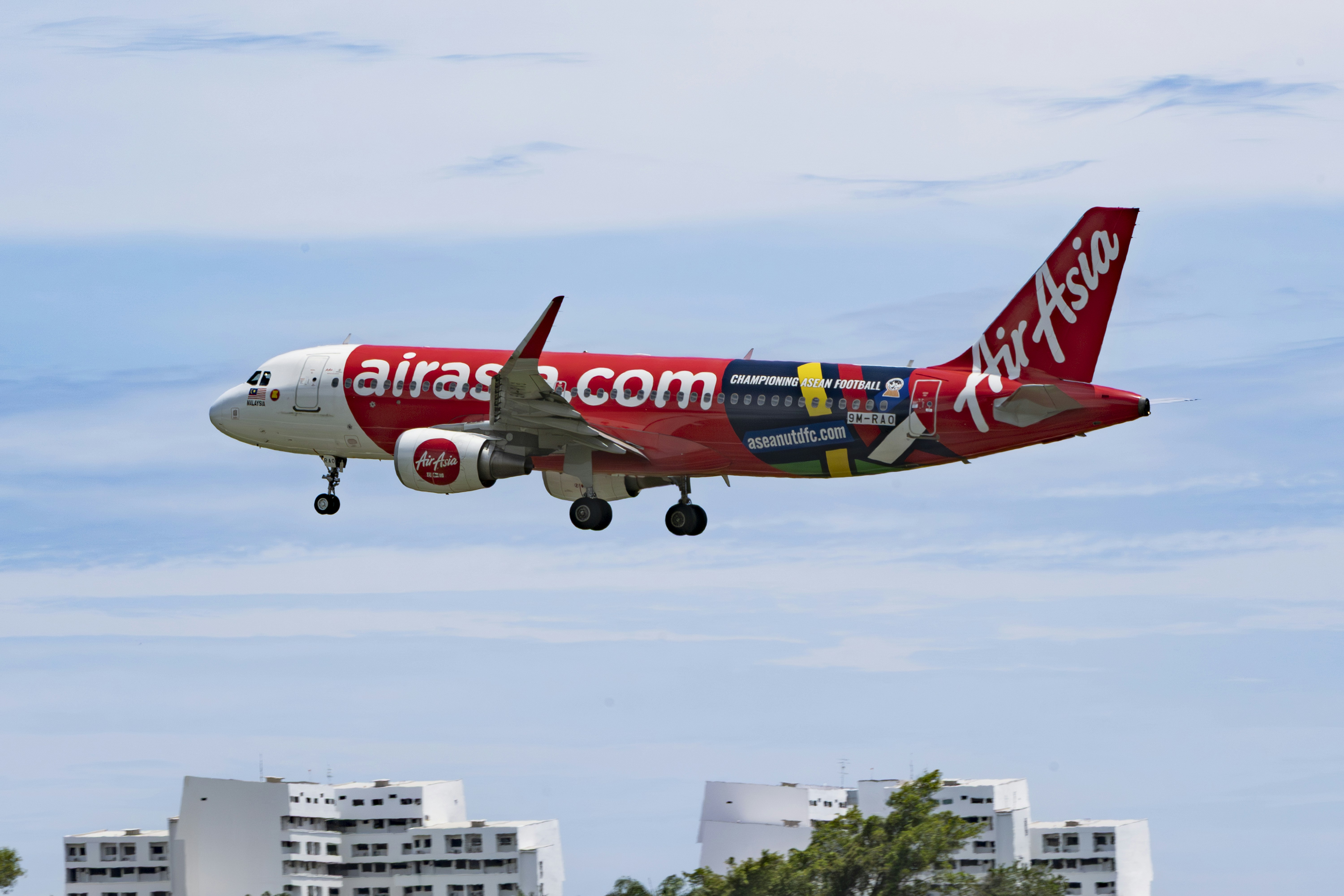 An airasia airplane flying over buildings under a blue sky. photo ...