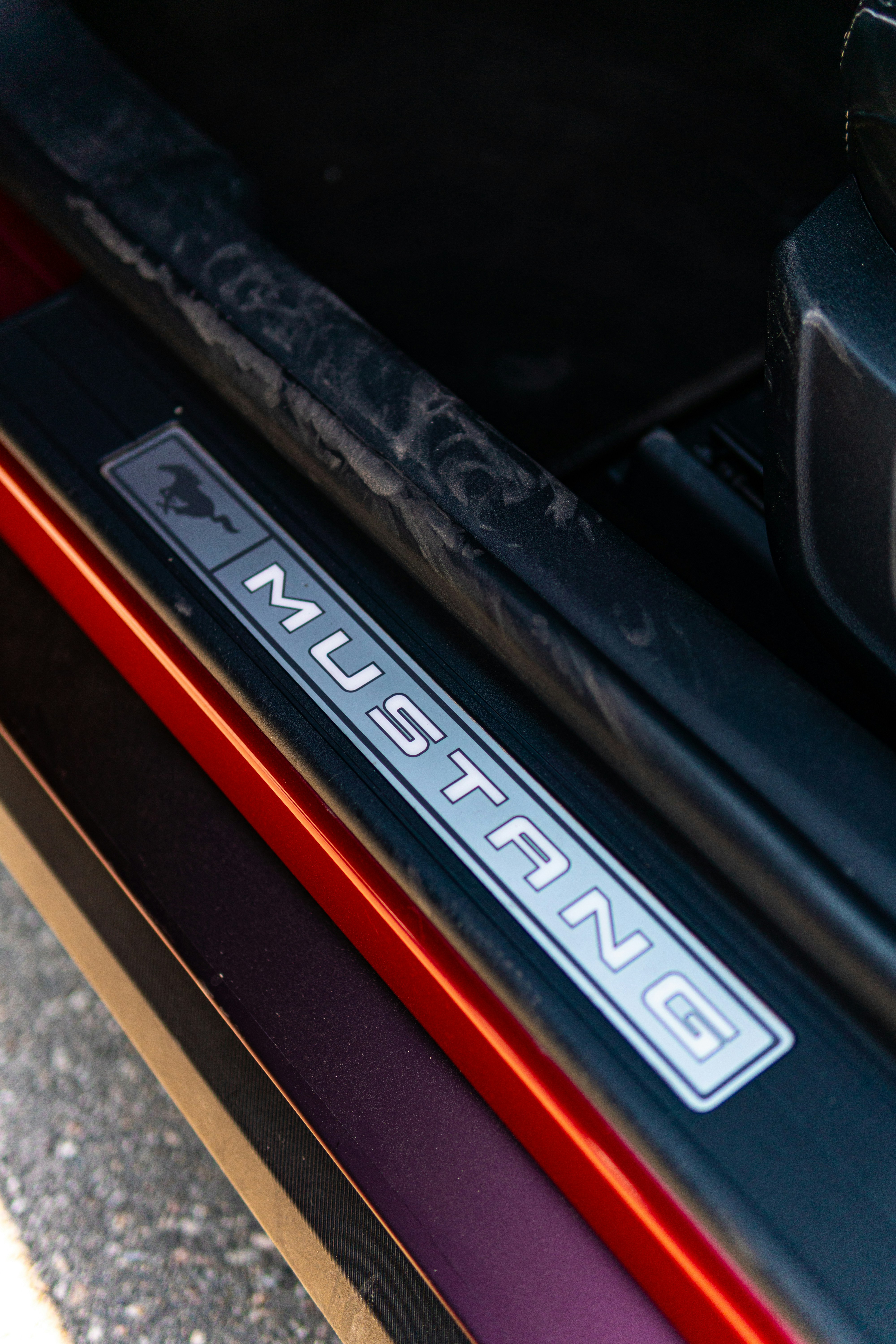 Metallic Badge, Red Trim, and Worn Threshold in a Car Trunk Sill