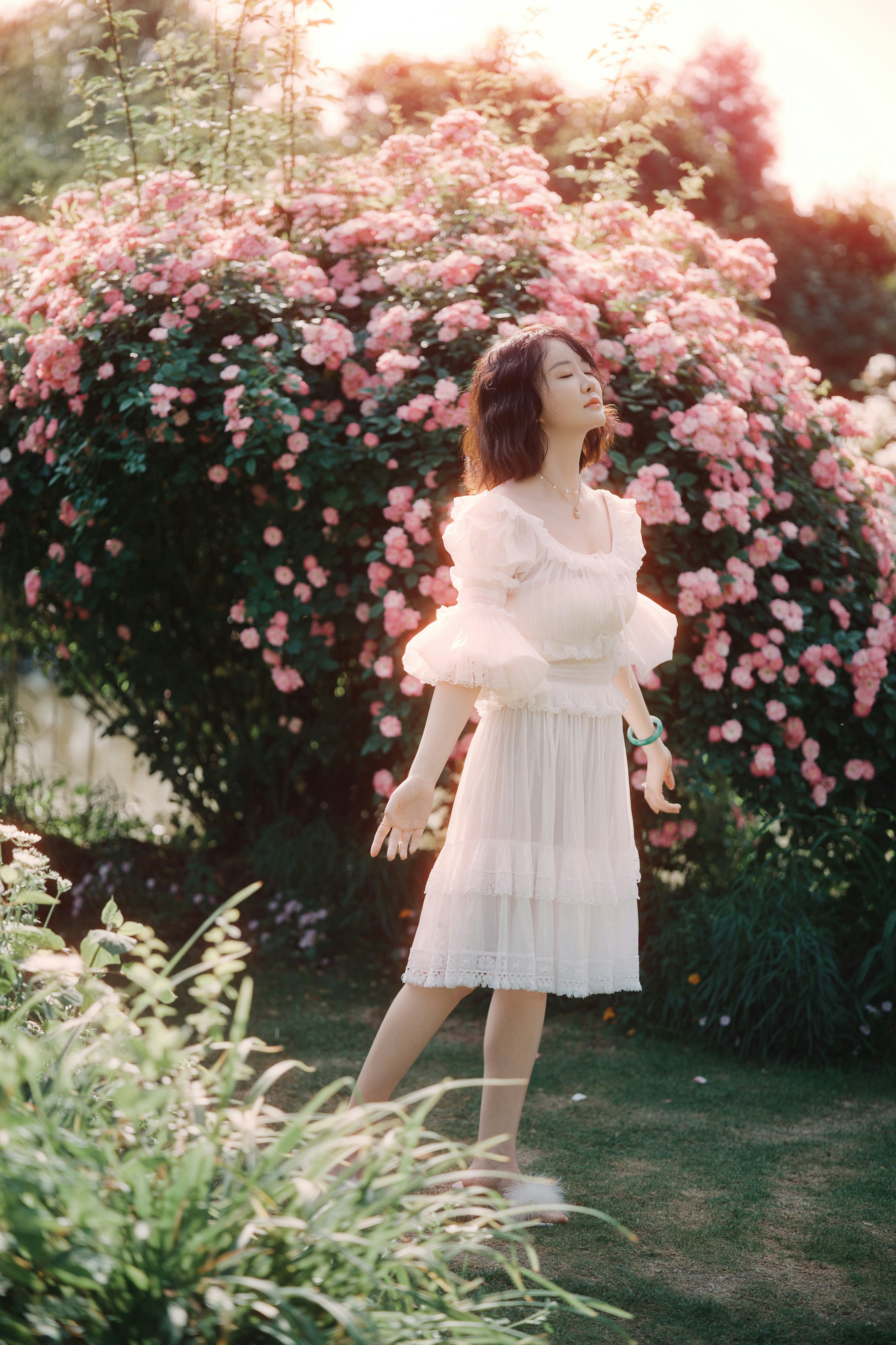 Sunlit Grace: Woman in White Amid Pink Blooms