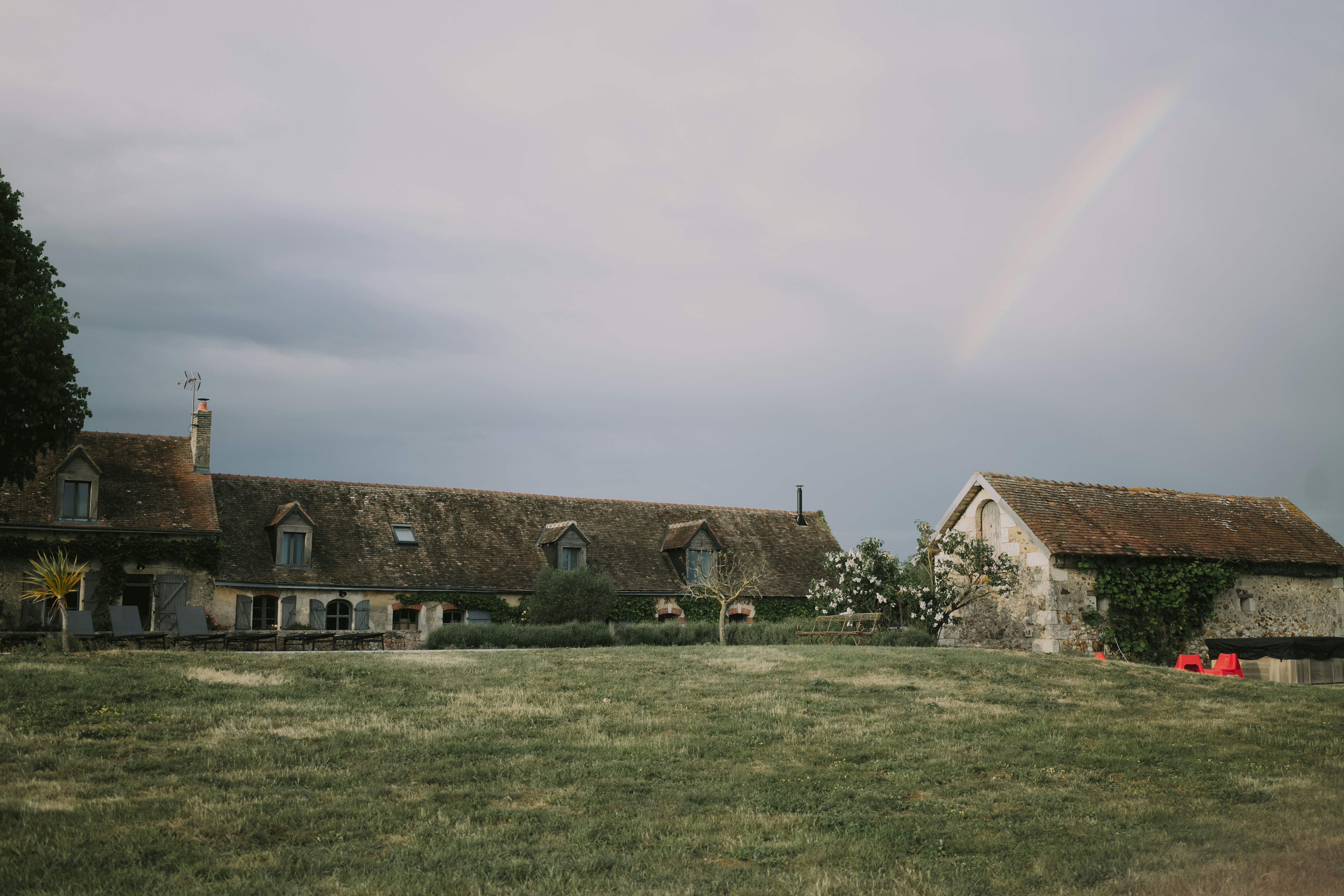 Rustic farmhouse and stone barn beneath a pale rainbow
