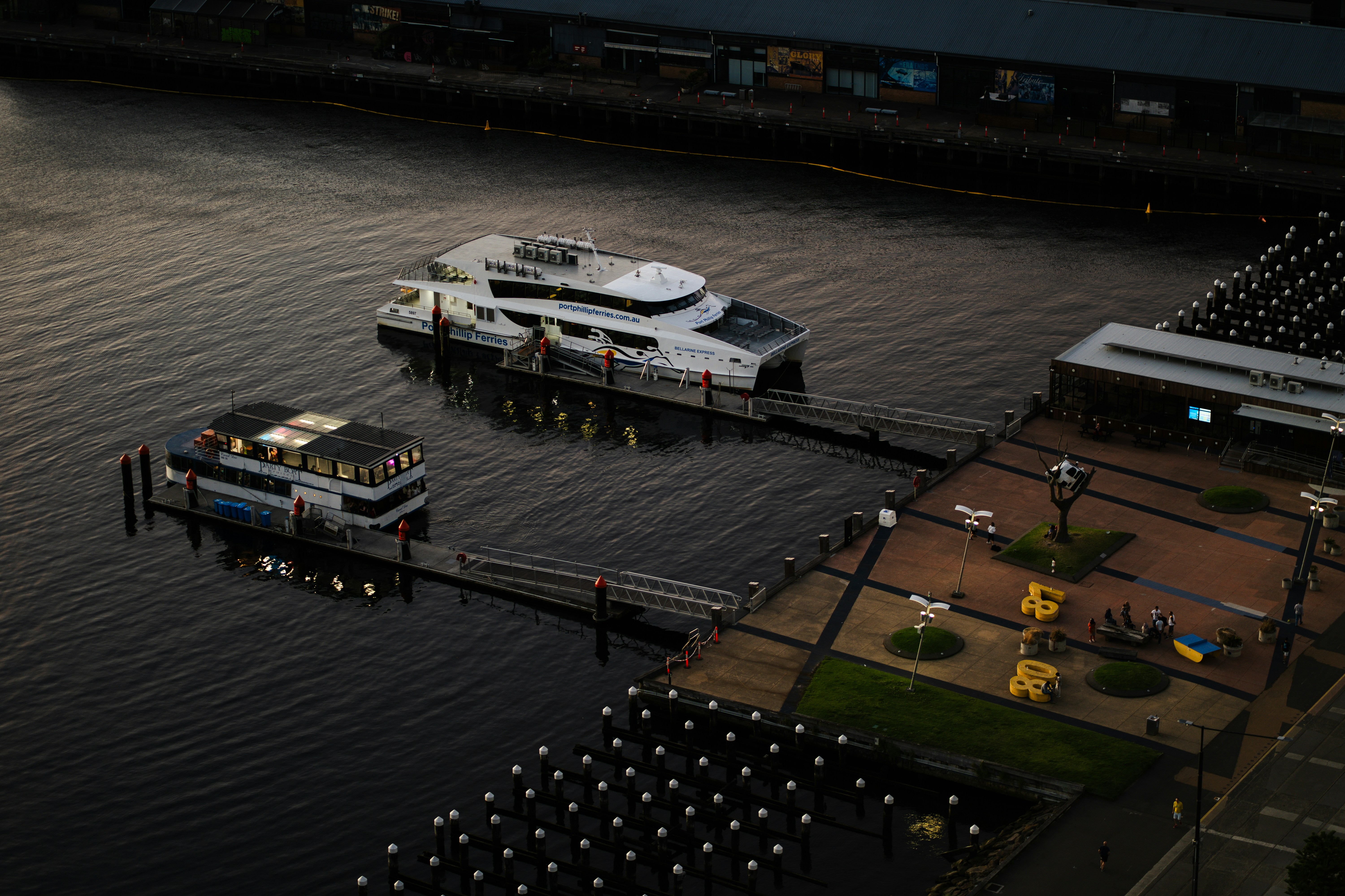 Docked Against the River: Aerial Portrait of Boats and Boardwalk Lights