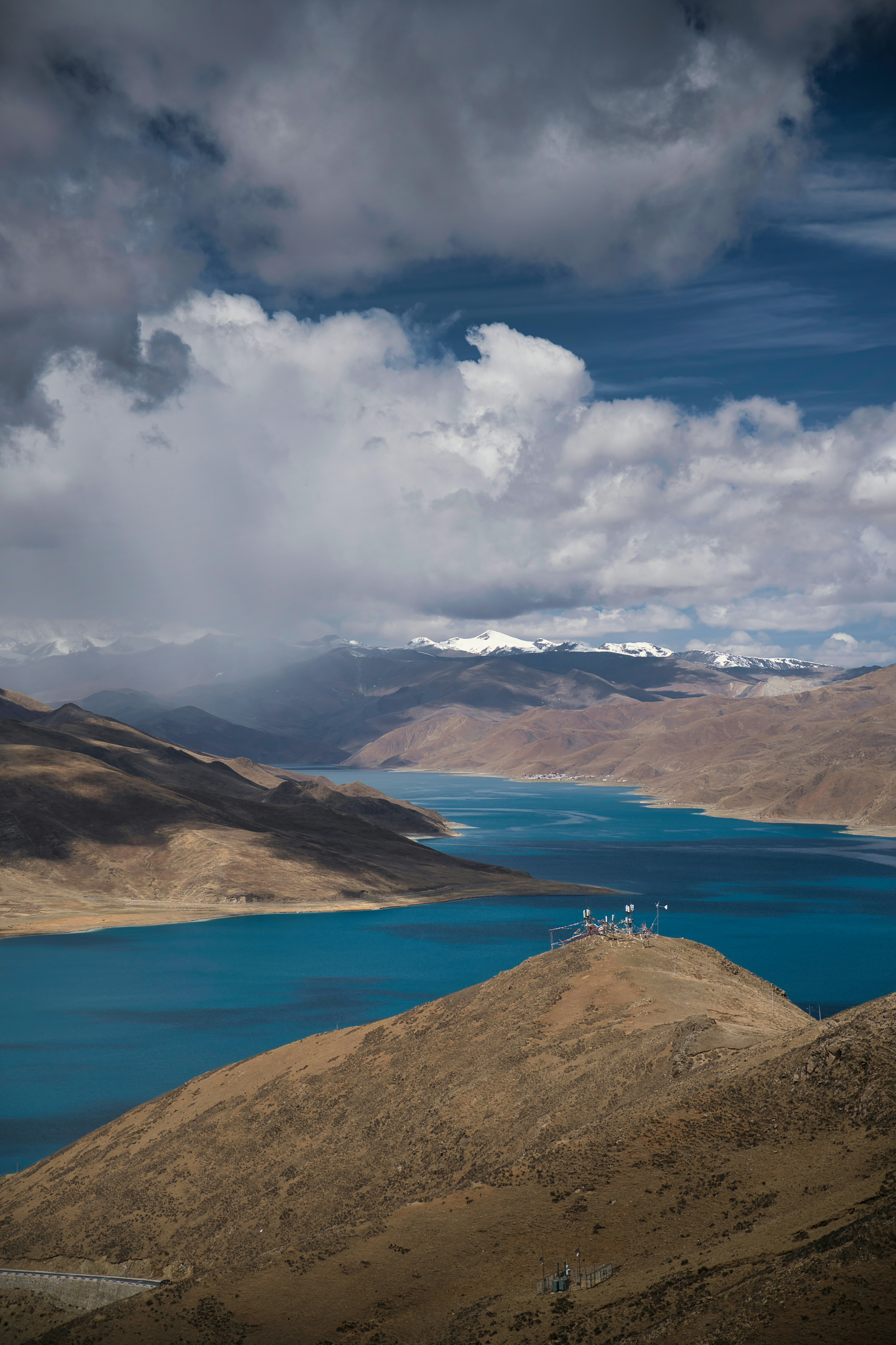 Blue lake, brown hills, distant snow-capped mountains, and cloudy sky.