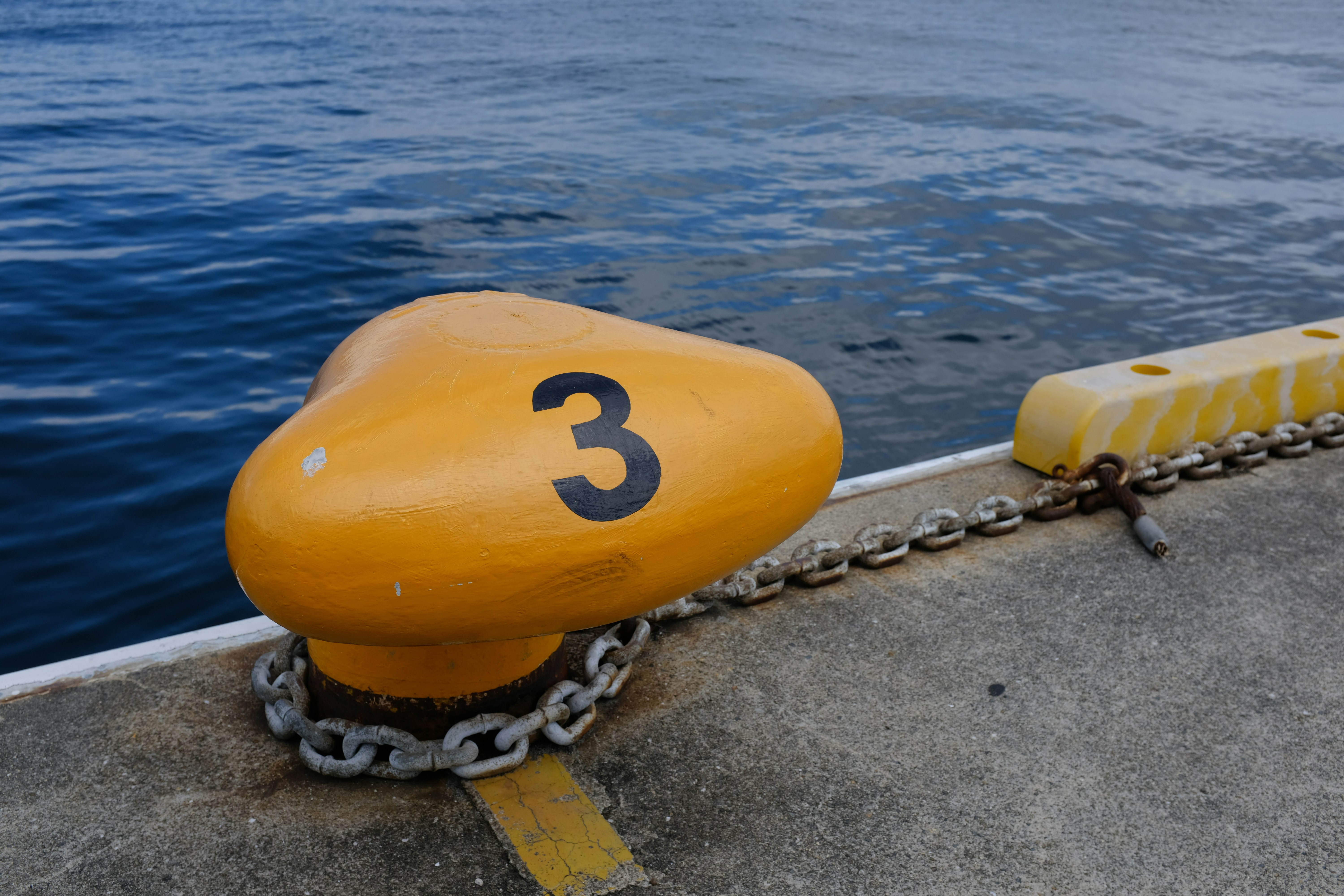 Yellow bollard with chain at harbor edge
