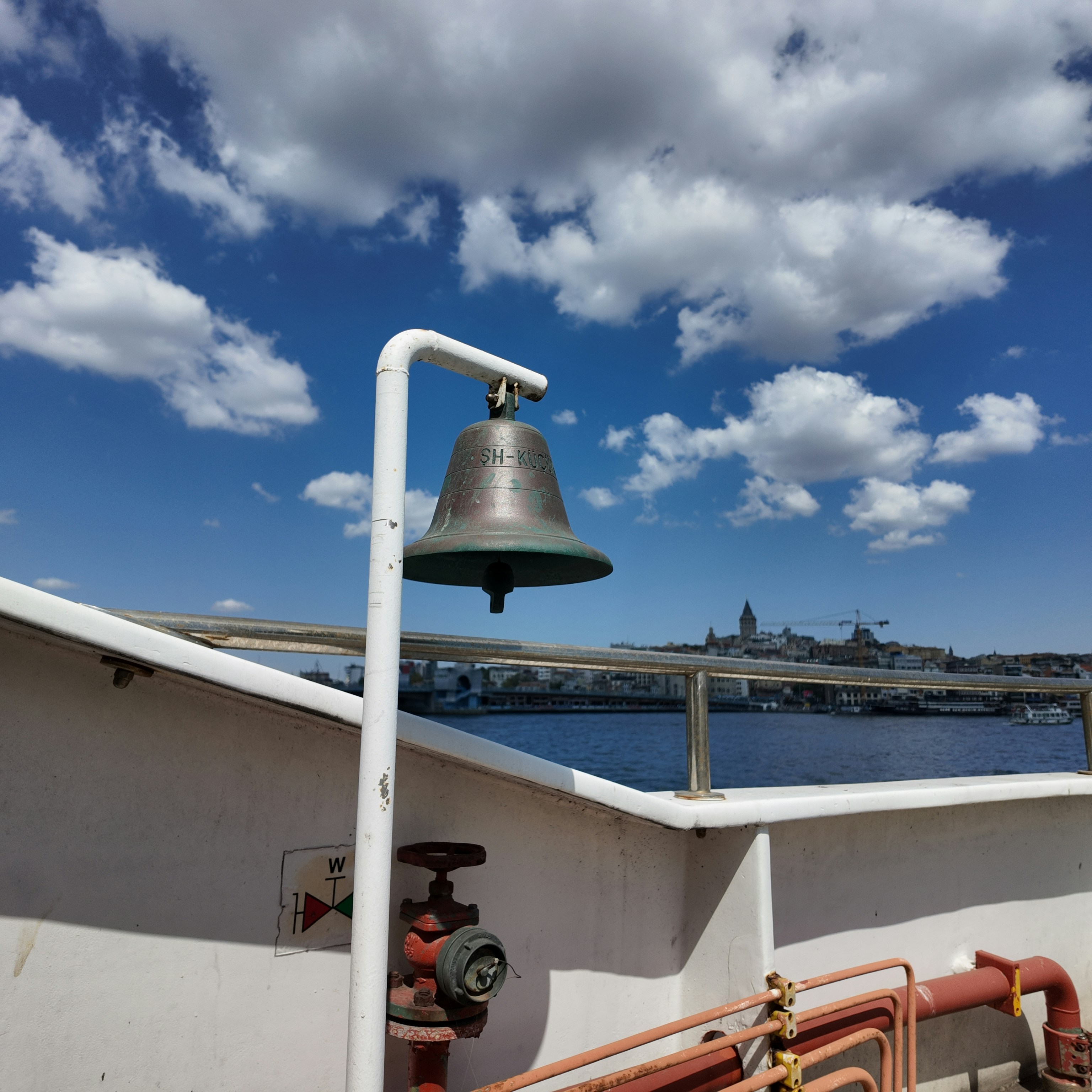 A lone bell over a harbor rail under a bright sky