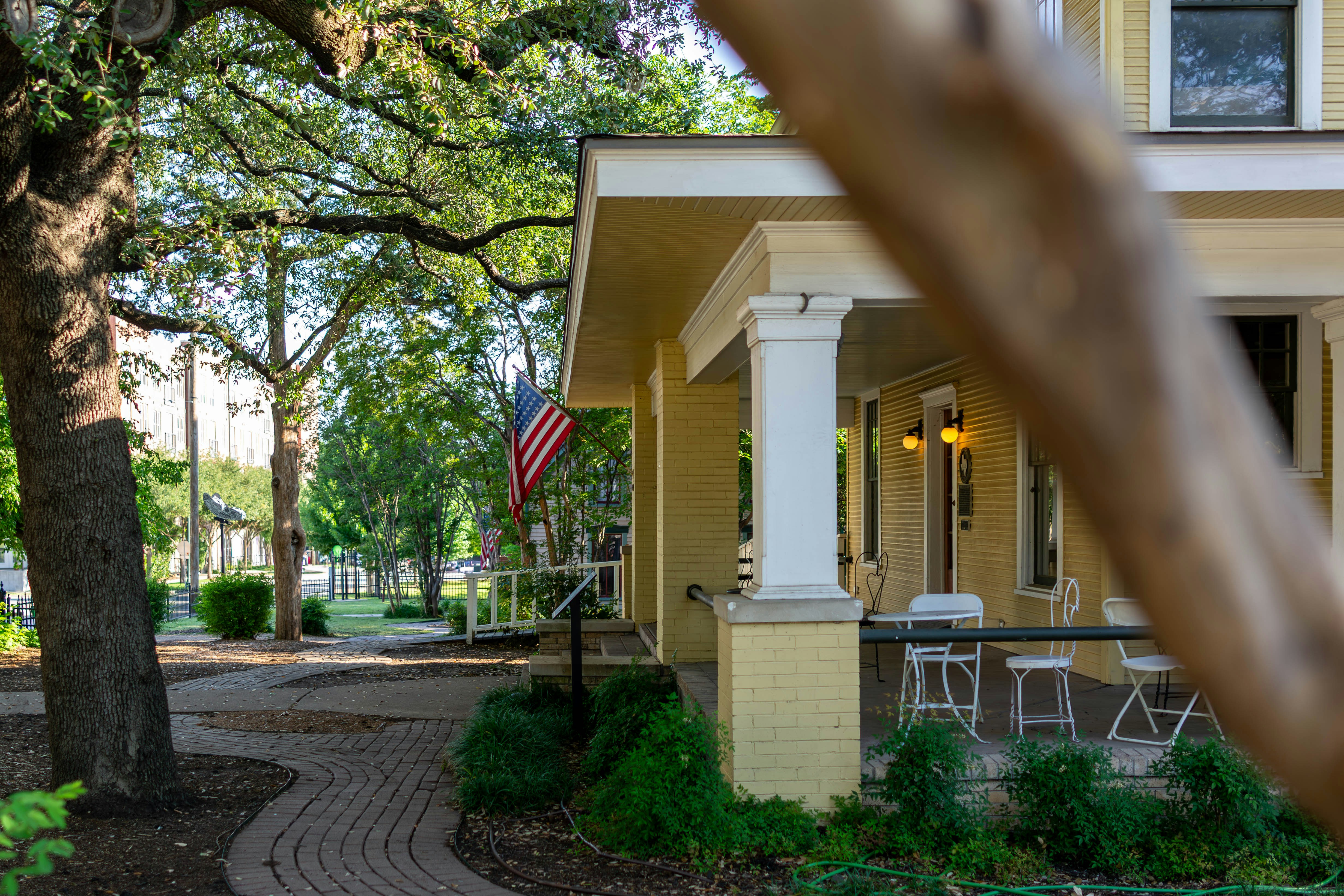 Sunny Porch of a Quaint House with Flag and Tree-lined Path