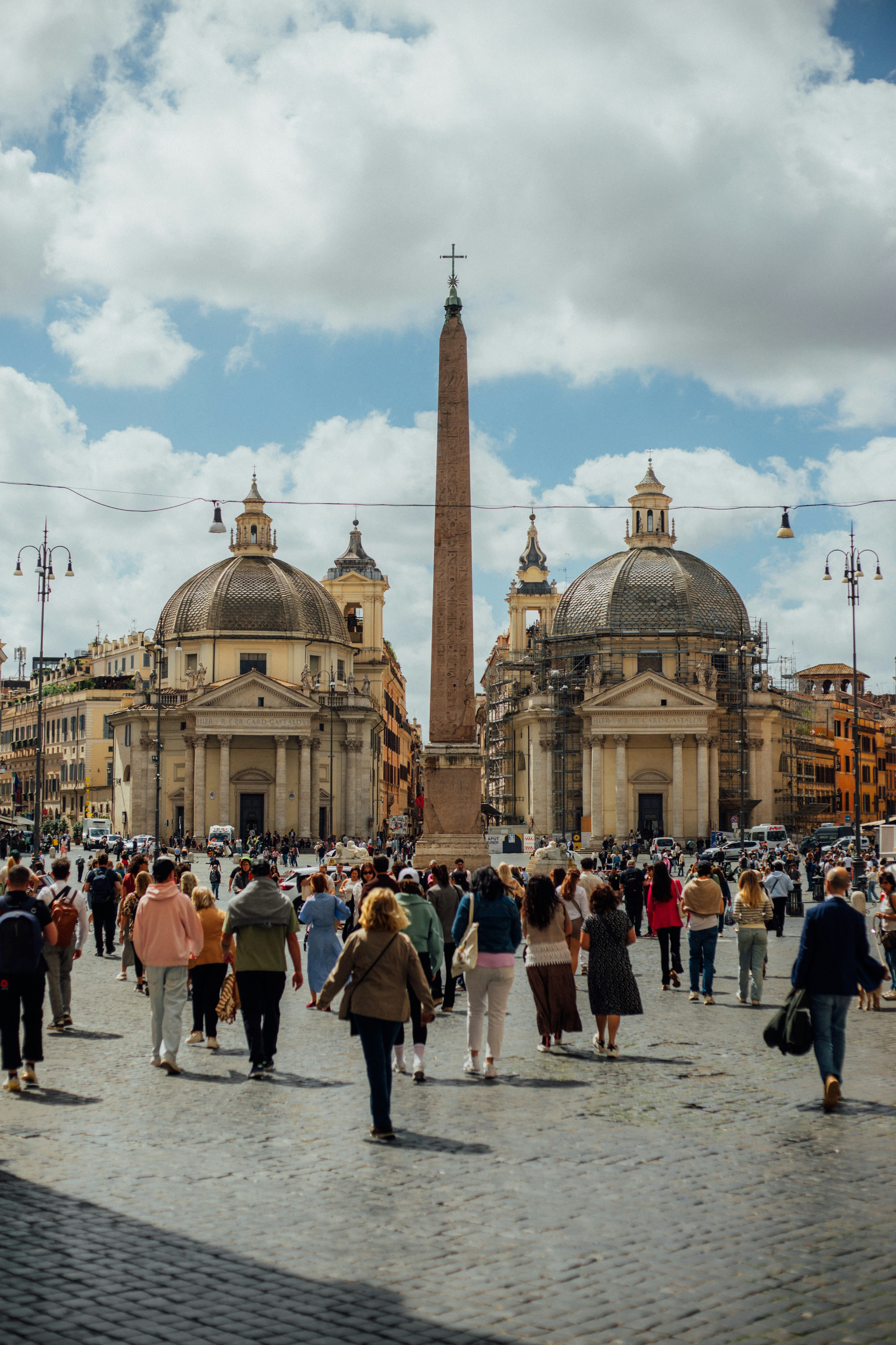 Crowd gathers before the Italian obelisk and twin domes in a sunlit Piazza