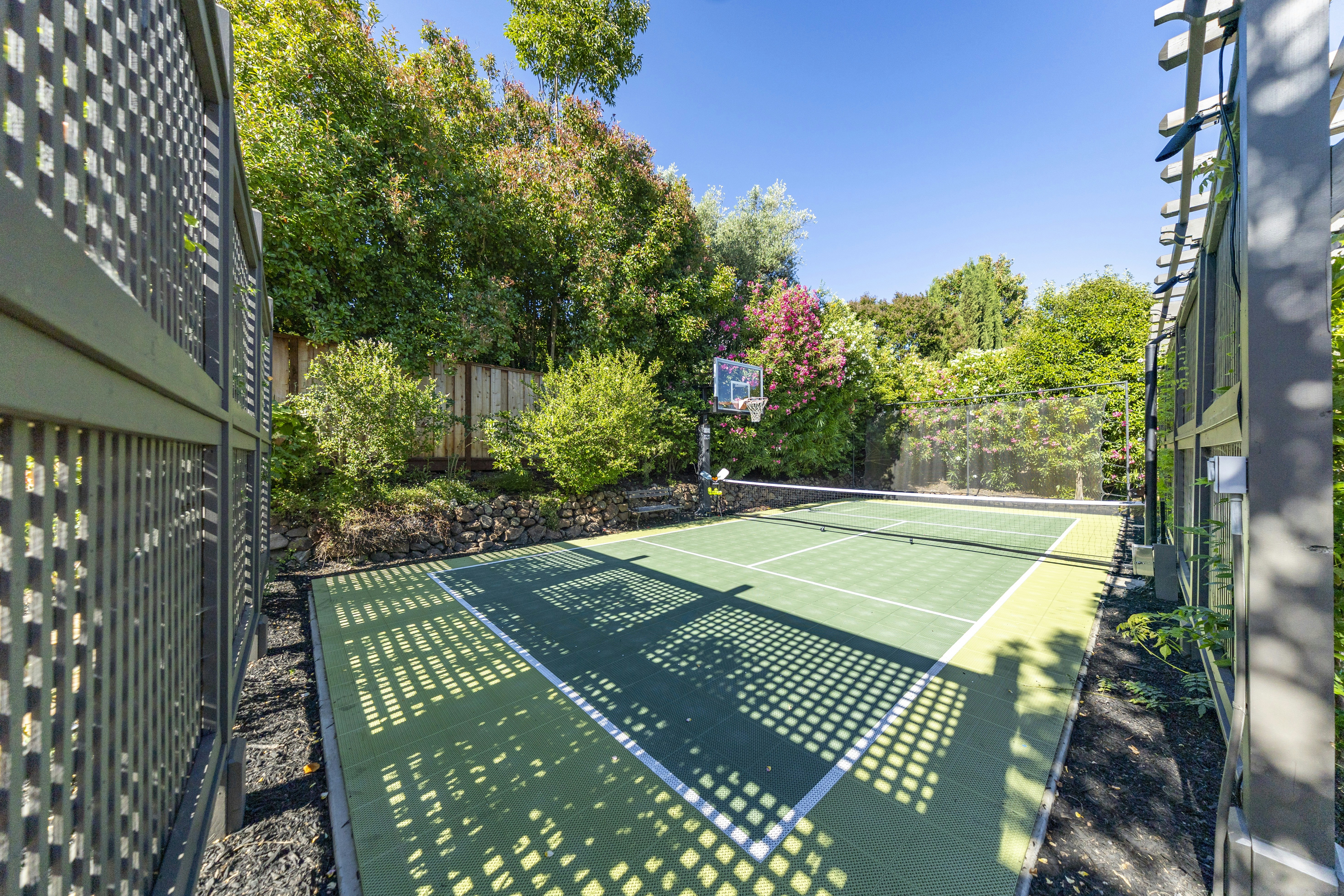 Sunlit pickleball court framed by green canopy and lattice shadows