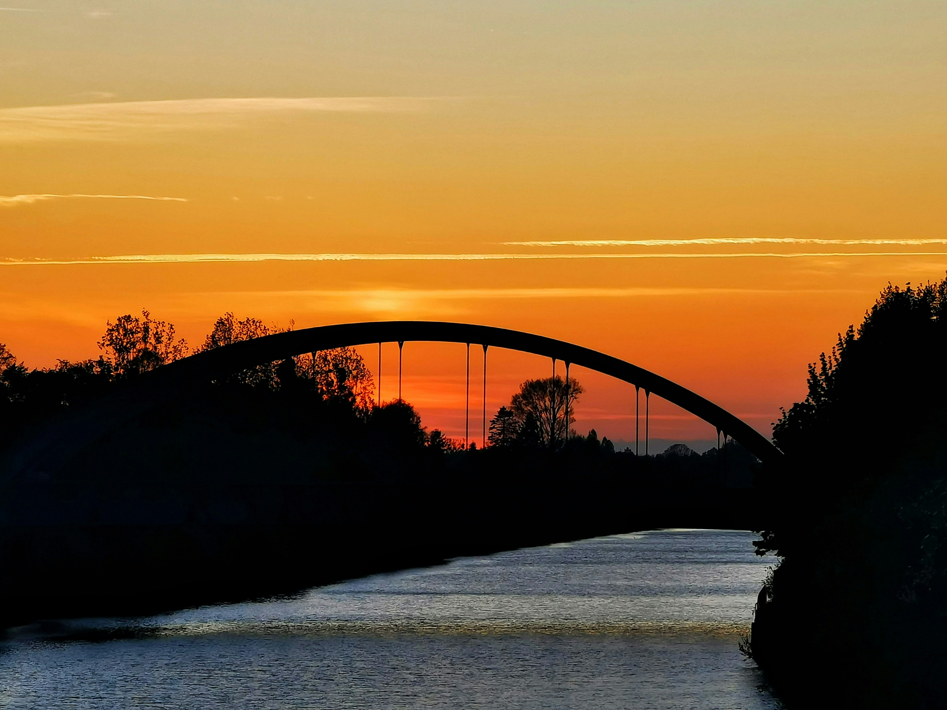 Evening Arc: silhouettes and a sunlit river under a graceful bridge