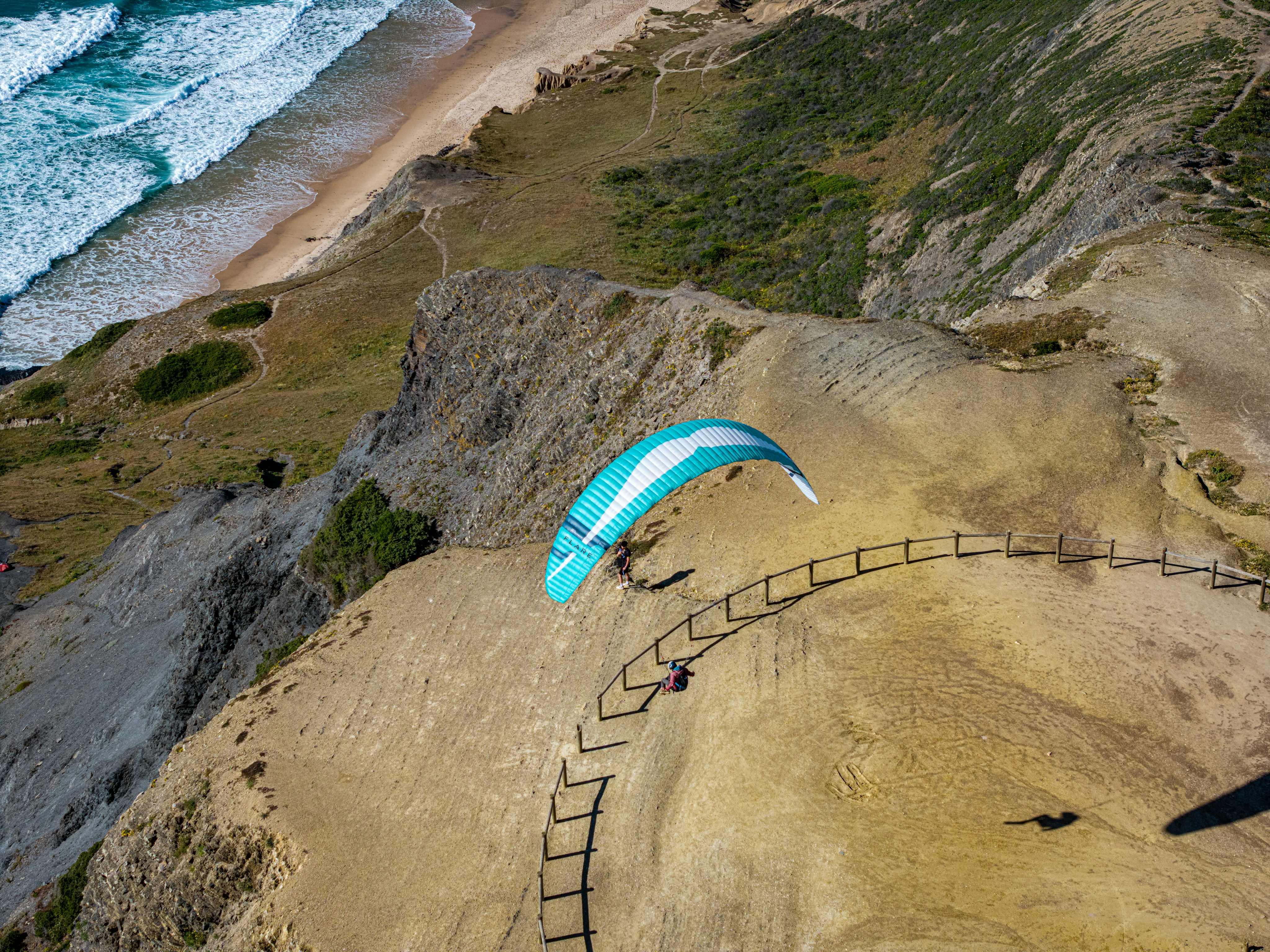 Blue Paraglider Arc Over Coastal Cliff