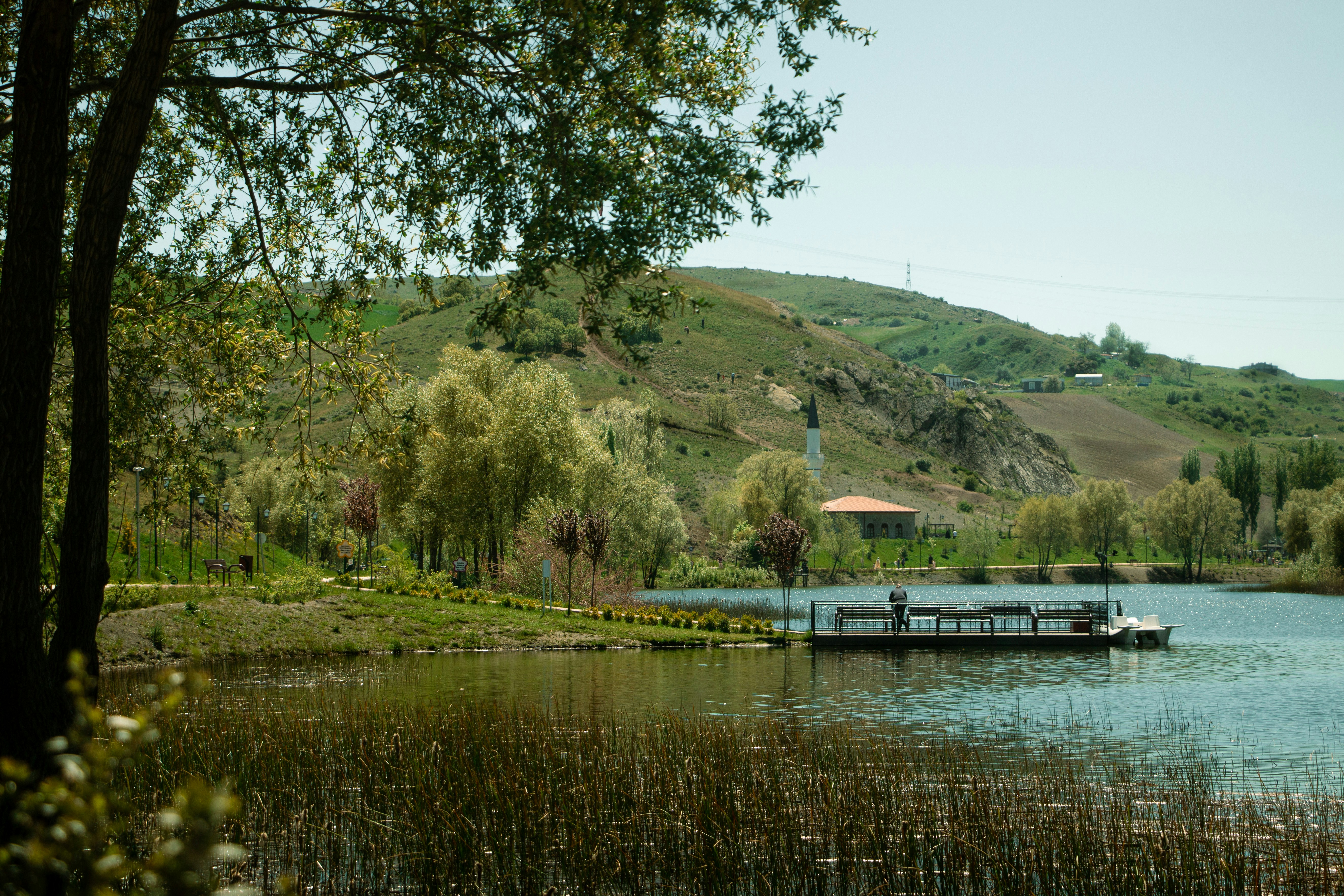 Calm lake with a dock extending from the shore, framed by trees and rolling hills in the distance.
