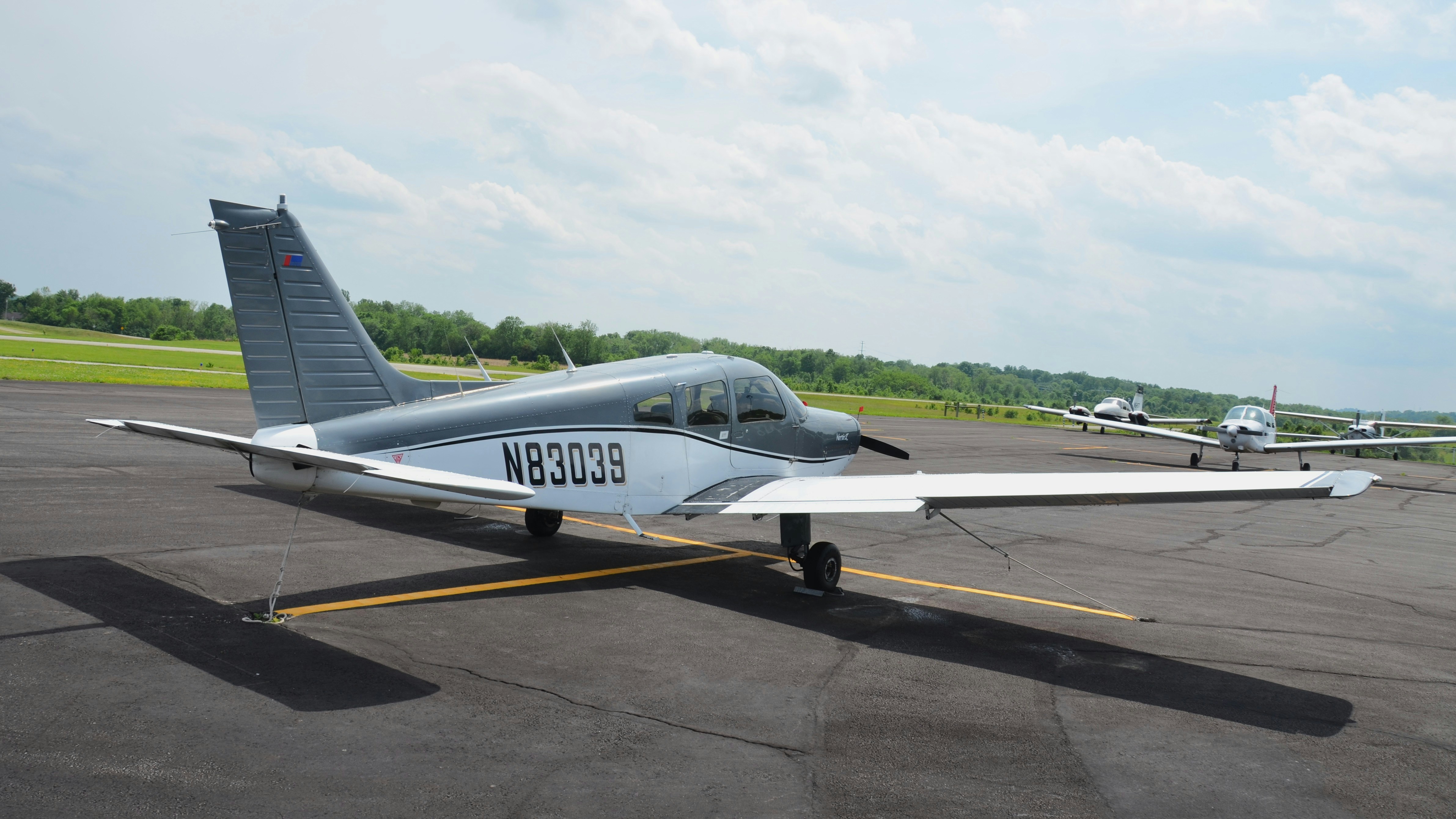 Navy-blue Cessna on a sunlit tarmac under a calm, cloudy sky