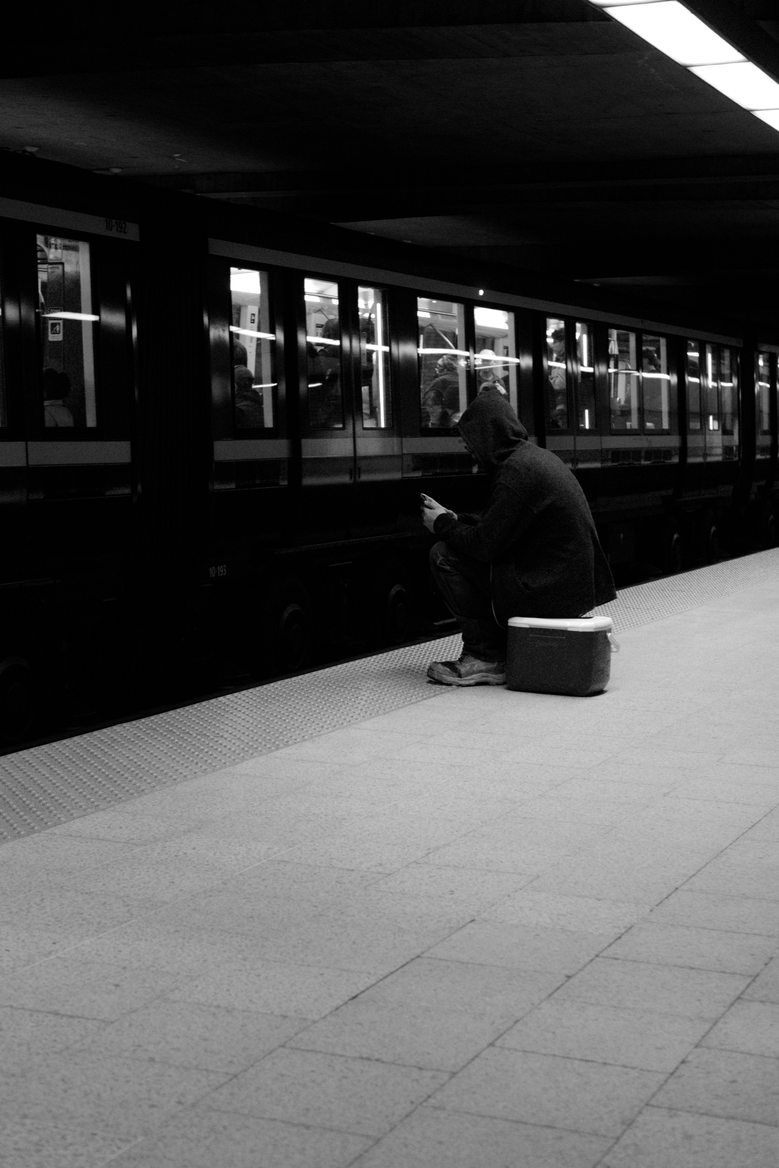 Hooded figure sits on cooler at subway platform. photo – Free Travel ...