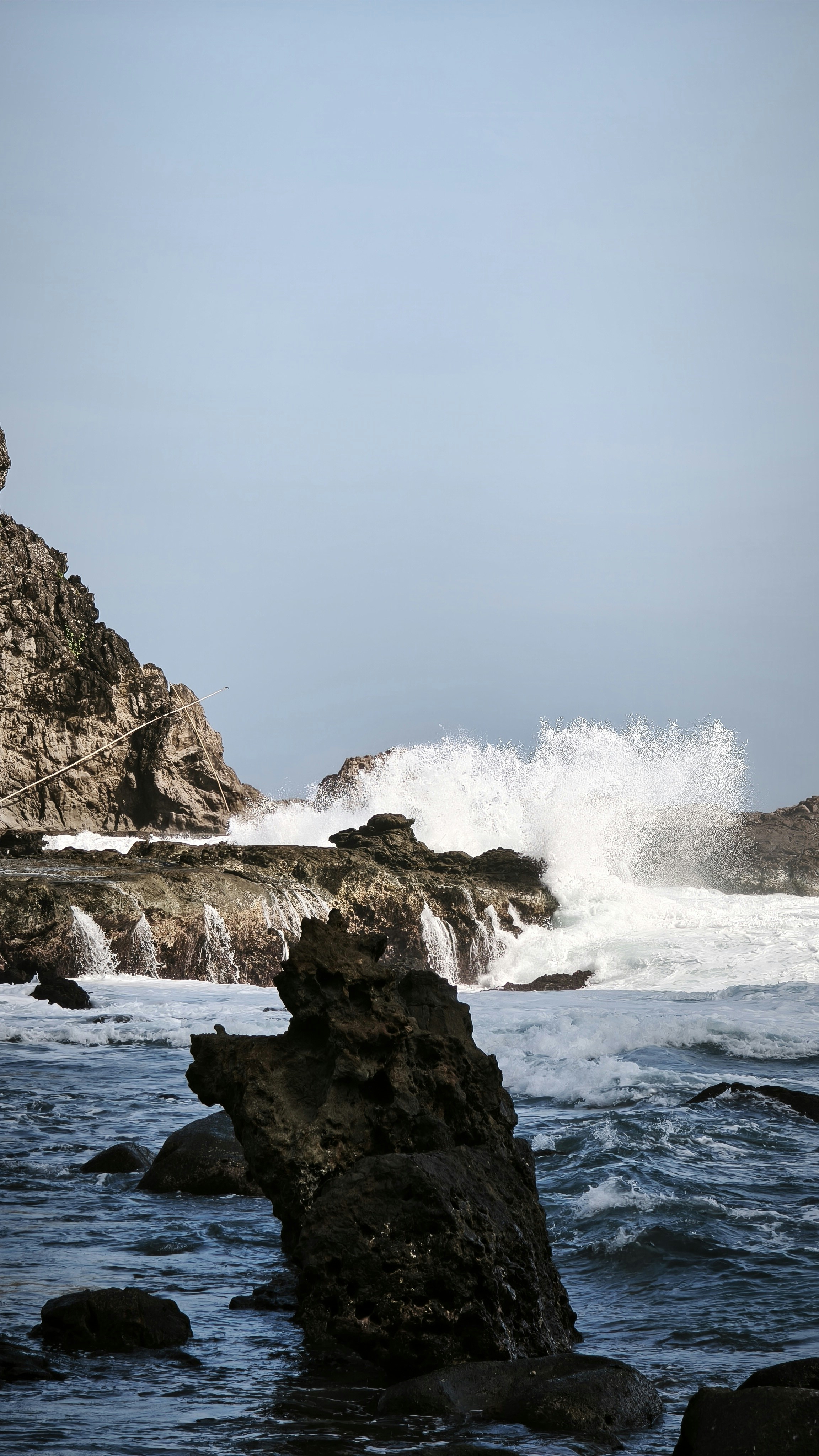 Ocean waves powerfully crash against dark, rugged coastal rocks.