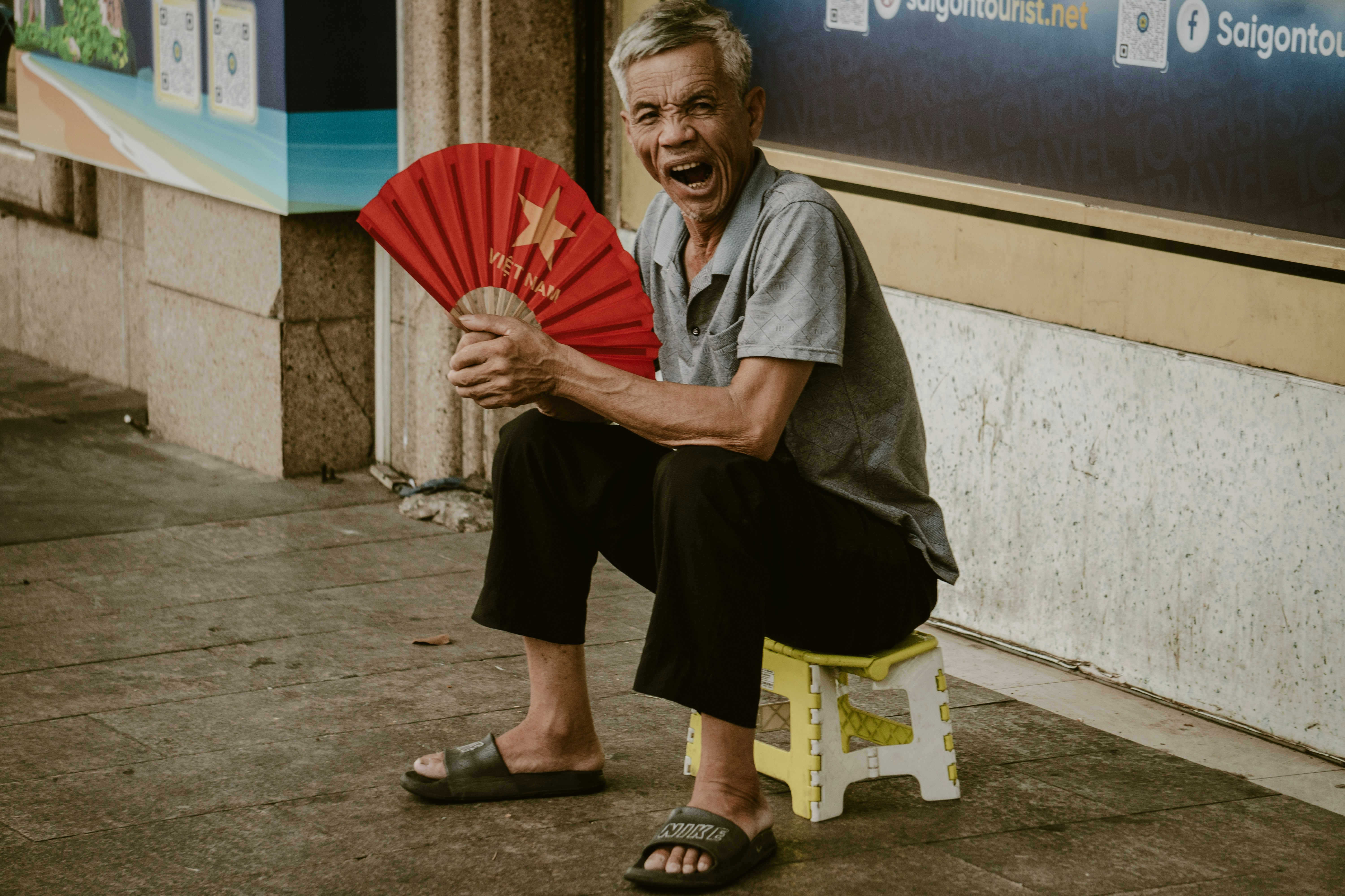Red Fan, Bright Laugh: A Street Performer Seated with a Cheerful Moment
