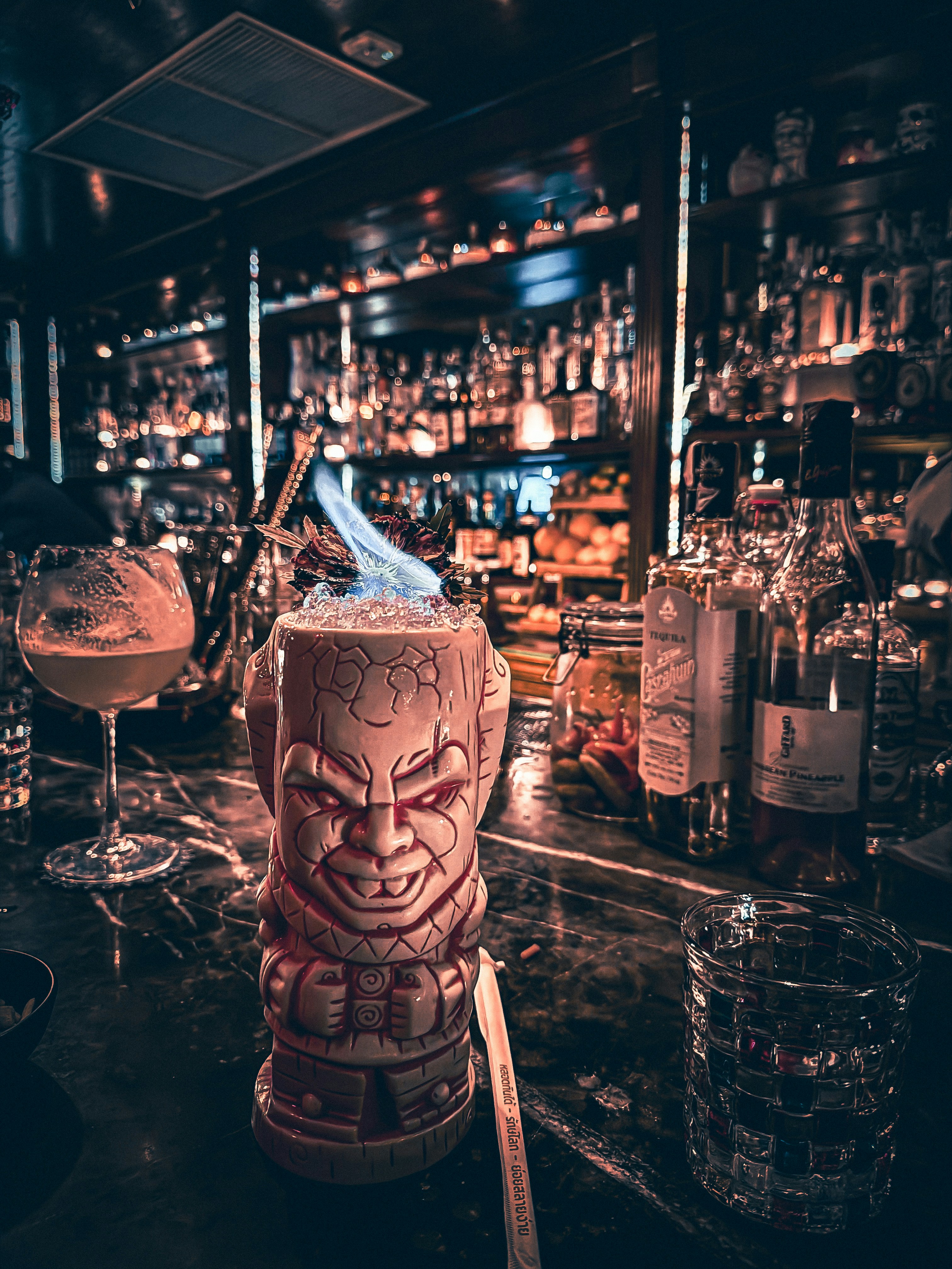 Neon-Bar Brew: A Carved Tiki Gaze Over the Bar